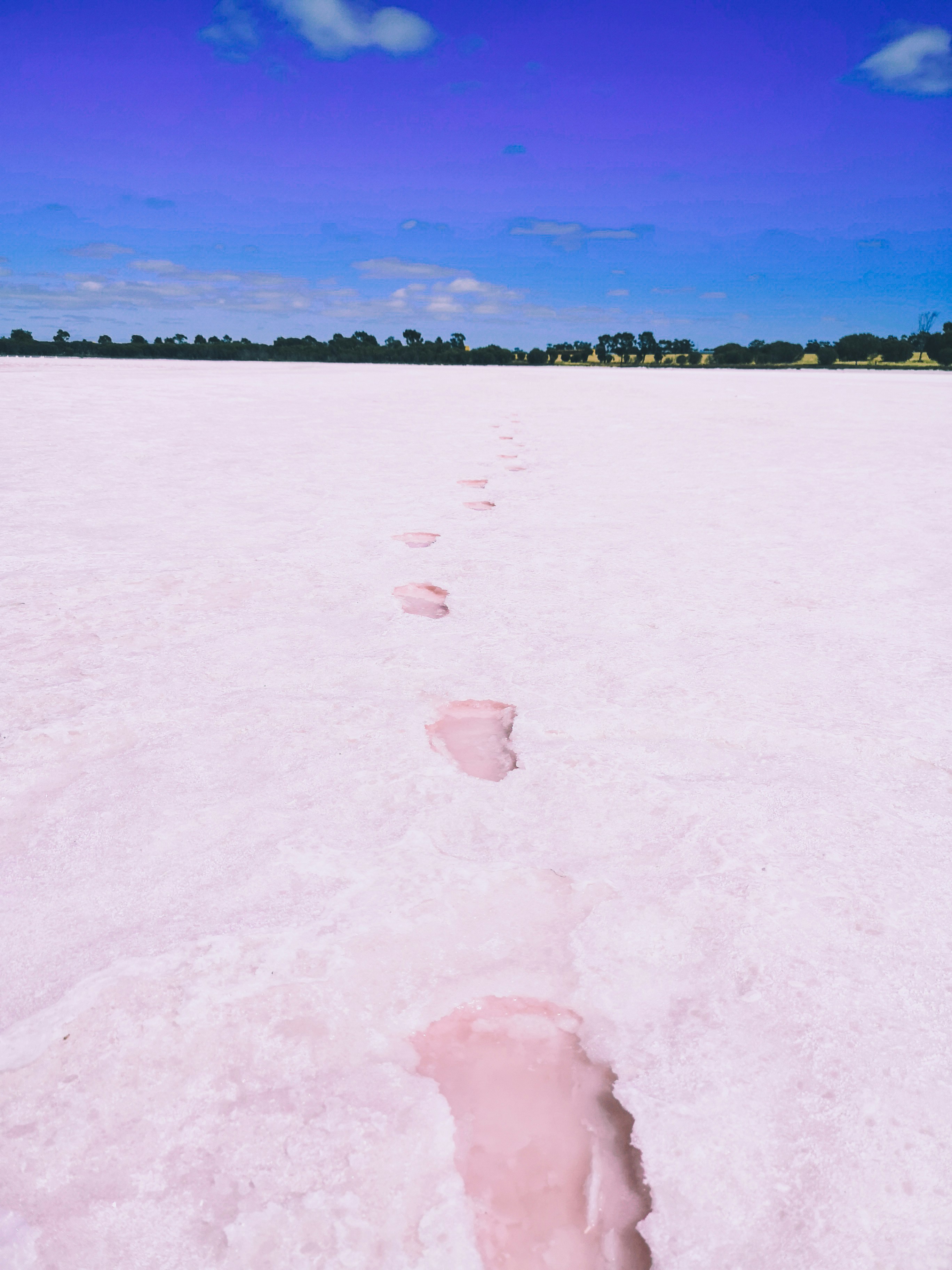 Footprints leading across a vast pink salt flat under a vibrant sky. The scene captures the unique landscape and tranquil atmosphere of the location.