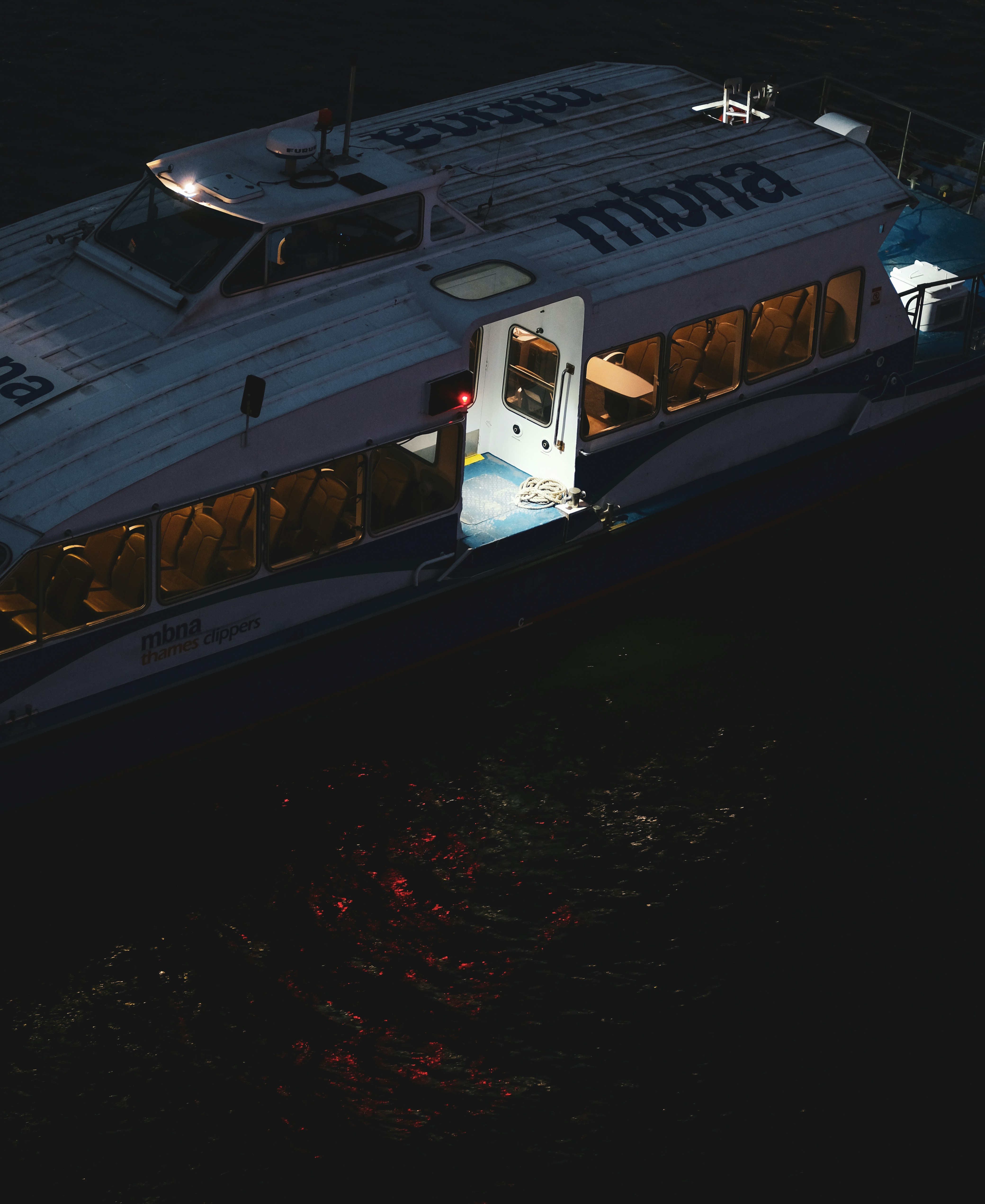 A ferry boat at night with an open door, revealing warm interior lighting against the dark water backdrop.