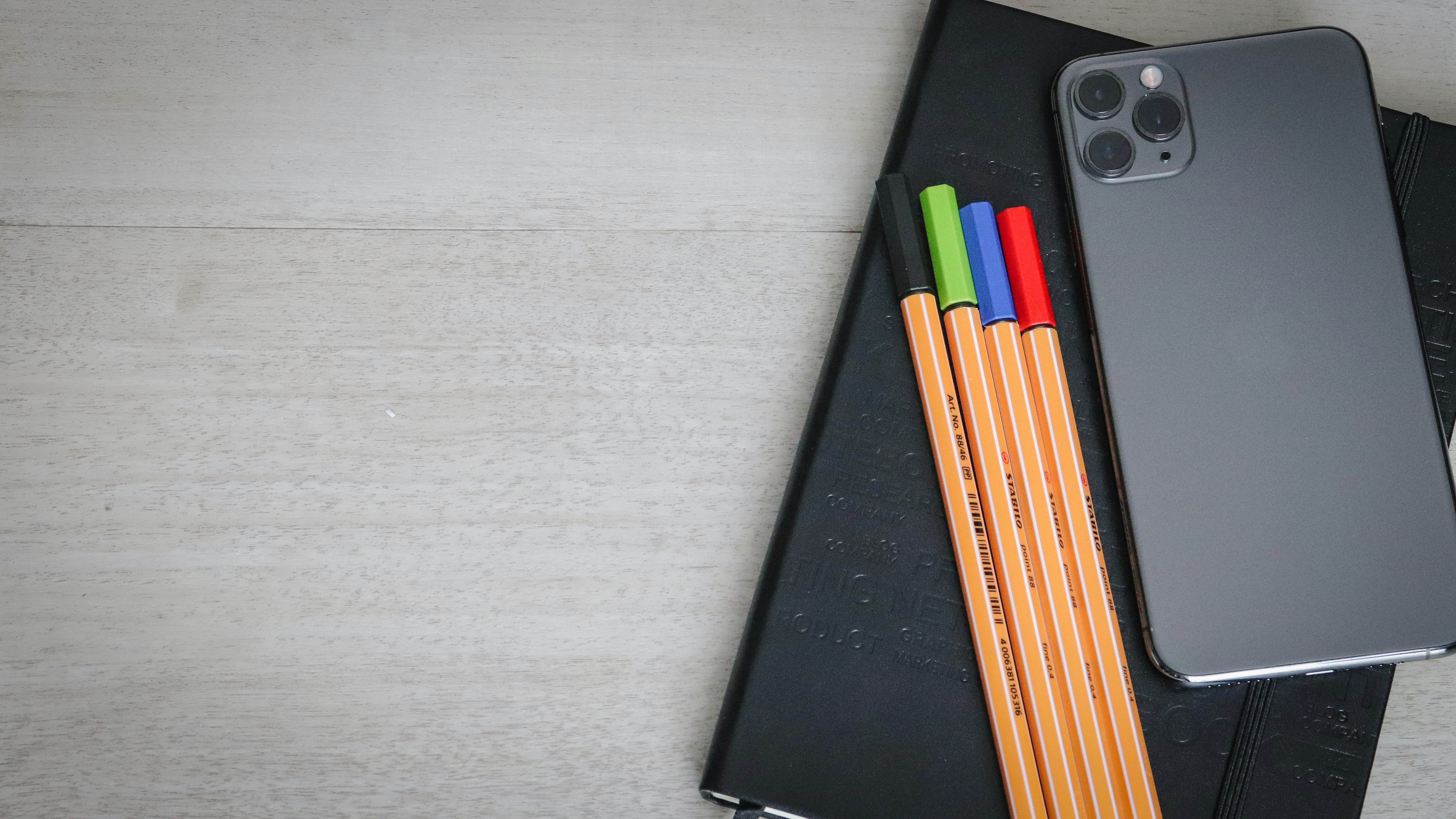 Lineup of Orange-Tipped Pencils Beside a Sleek Smartphone on a Pale Wooden Desk