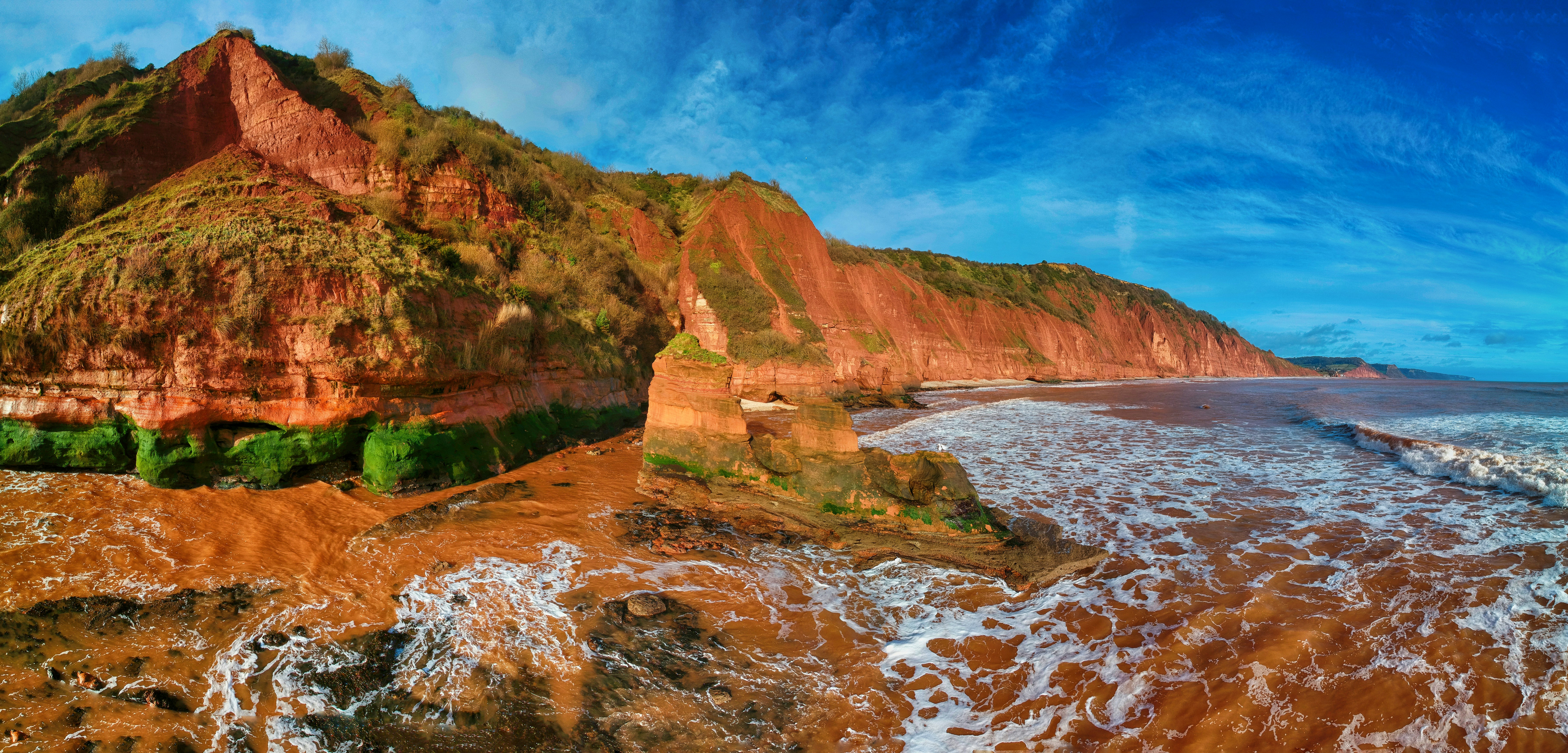 Crimson Cliffs and Ocean Foam: A Sunlit Coastal Panorama