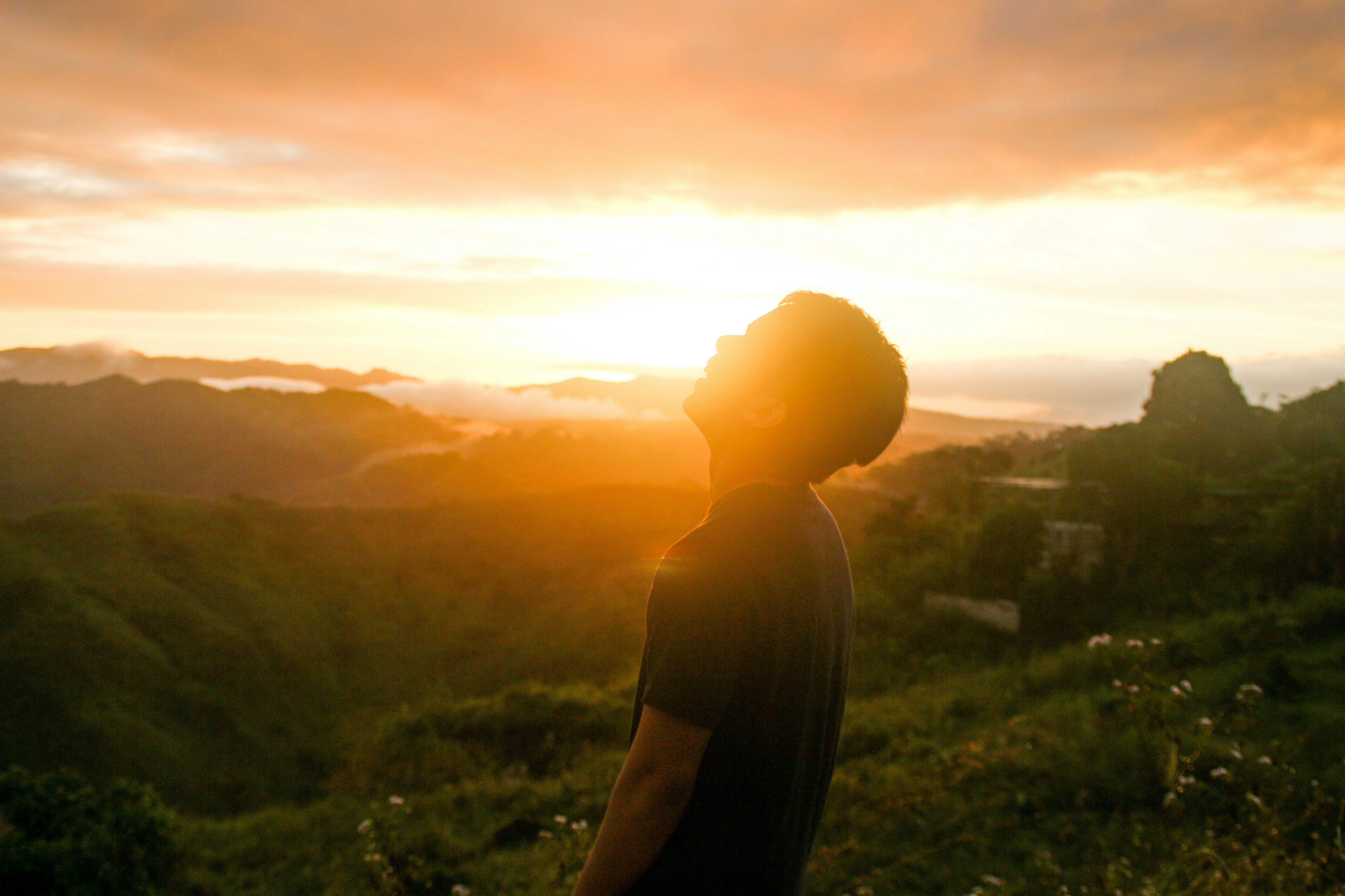 Silhouette of a person gazing upward against a vibrant sunrise over a mountainous landscape.