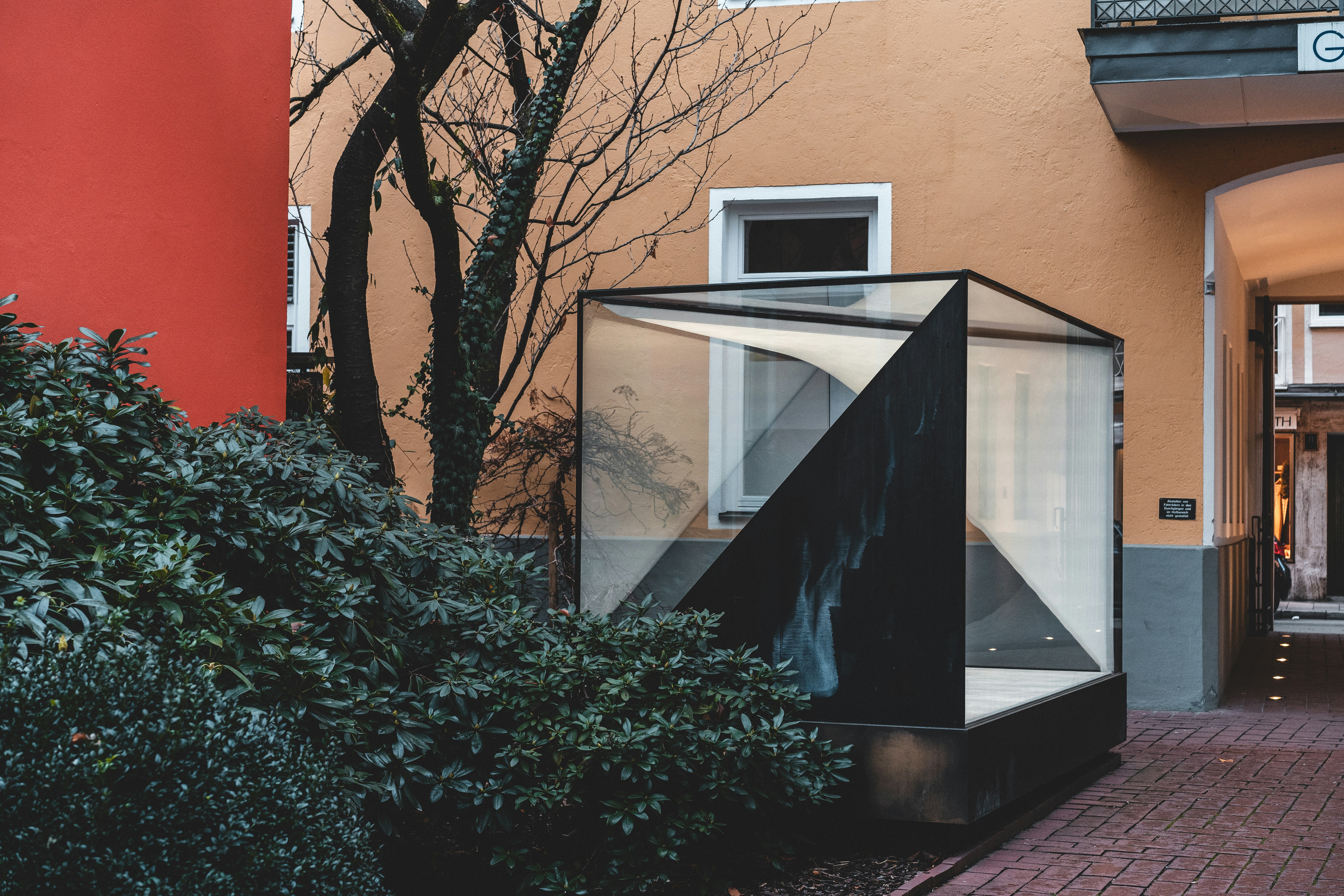 Modern glass display structure nestled among greenery and urban architecture, showcasing a blend of nature and design.