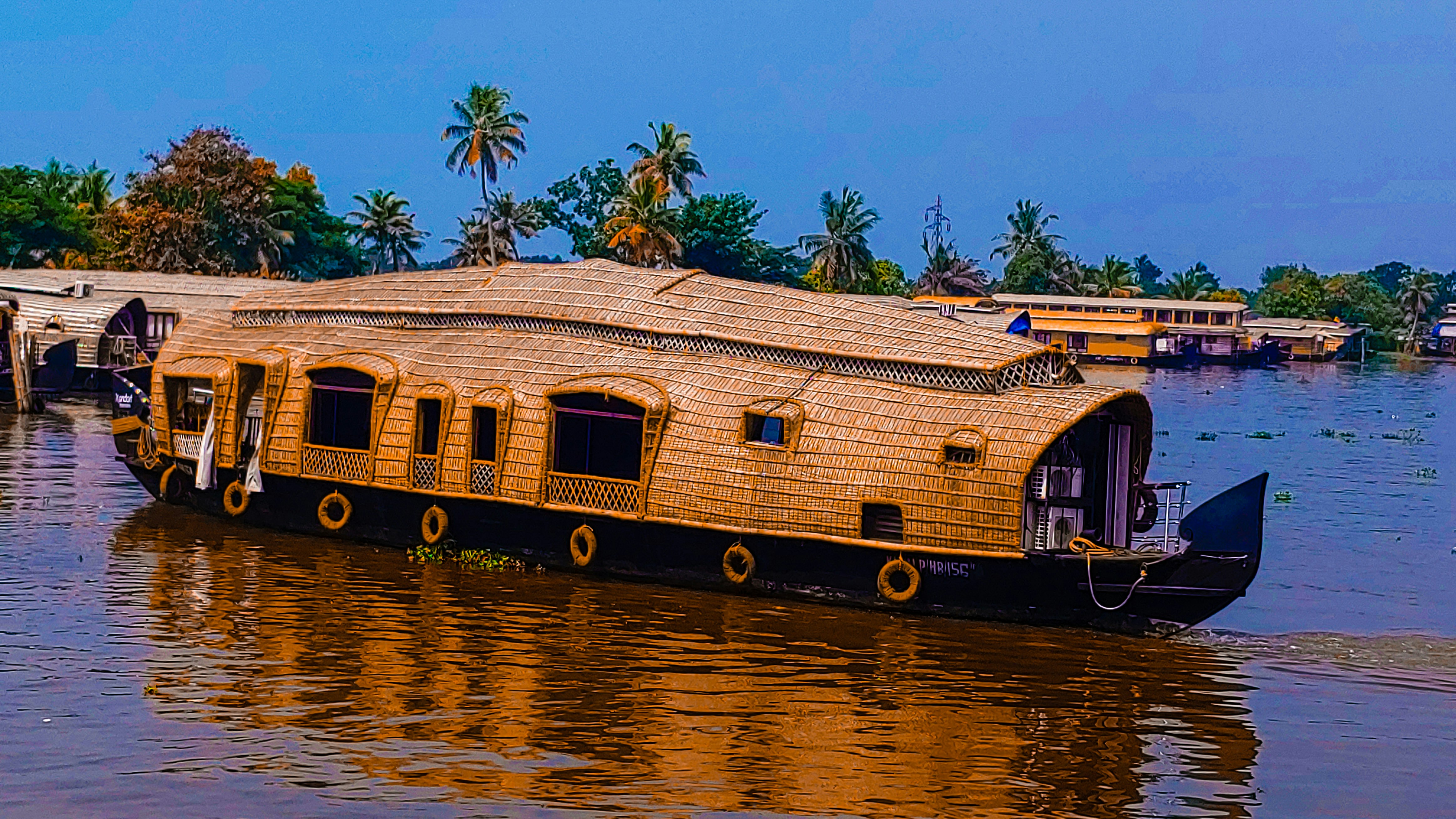 Traditional bamboo houseboat gliding on tranquil waters, surrounded by lush palm trees and vibrant scenery.