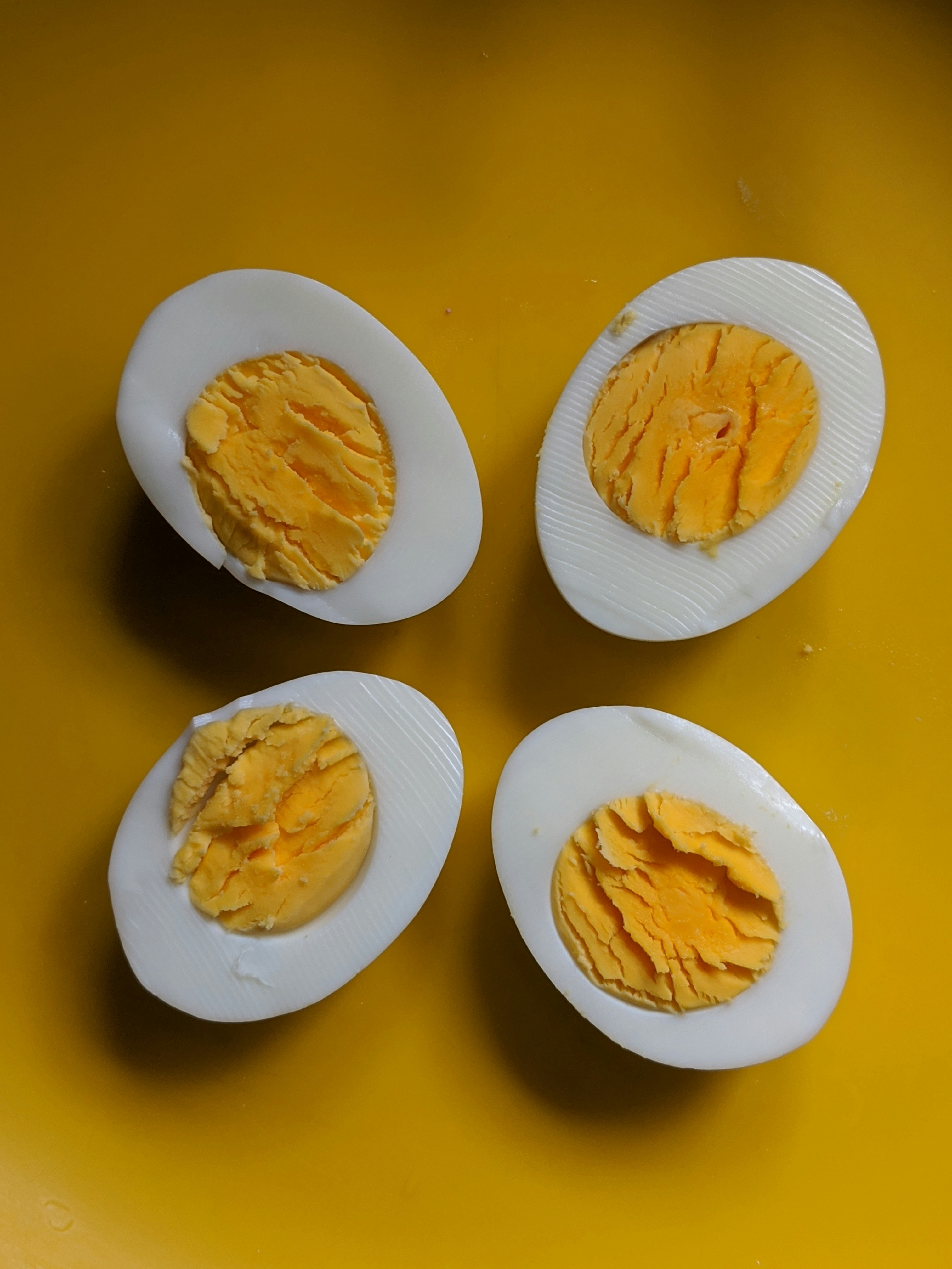 Four halved hard-boiled eggs arranged on a vibrant yellow surface, showcasing their creamy yolks and textured whites.