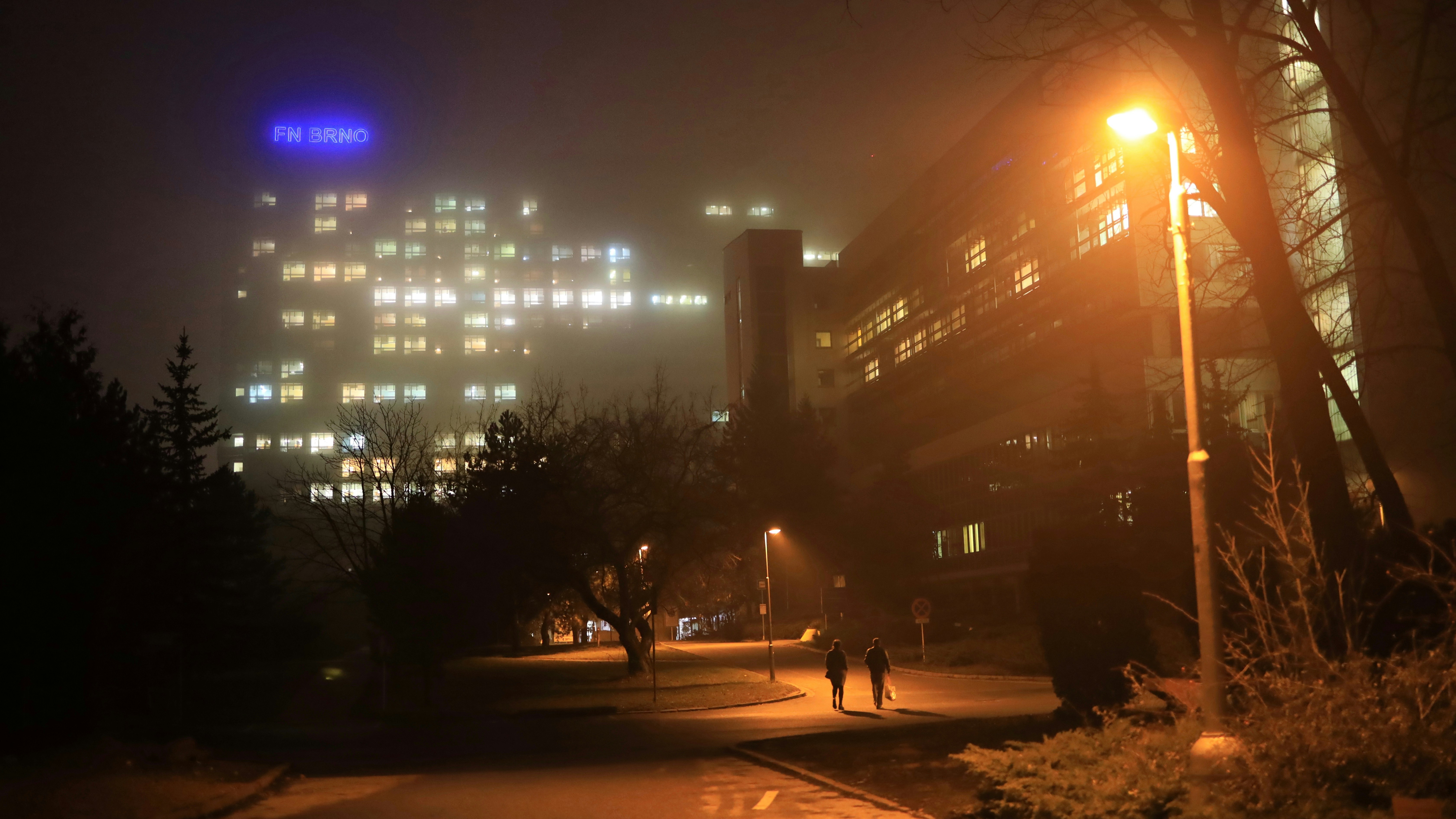 Foggy street lit by orange streetlights with silhouetted figures and a glowing building in the background.