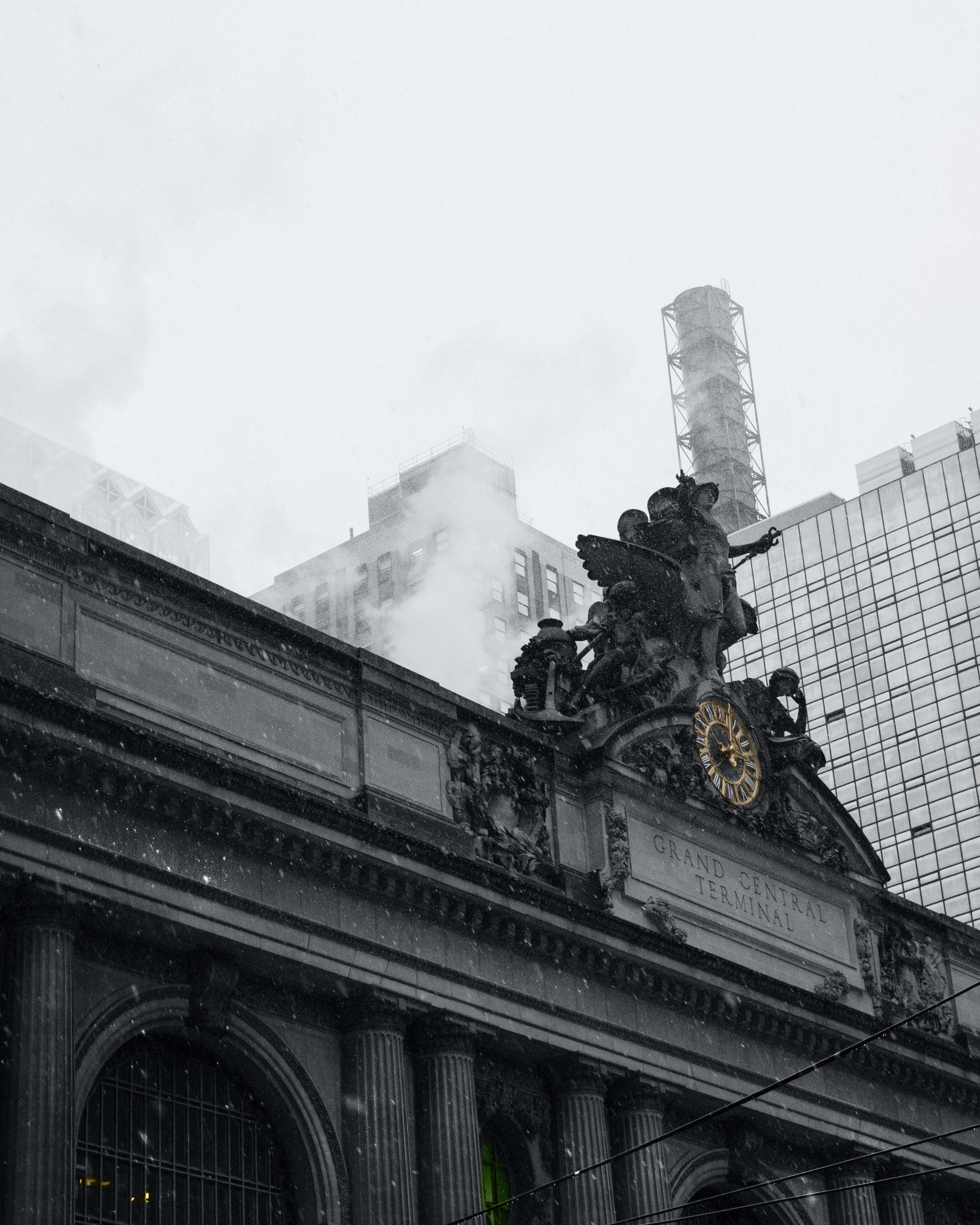 Historic Grand Central Terminal adorned with intricate architectural details, partially obscured by falling snow and urban mist.