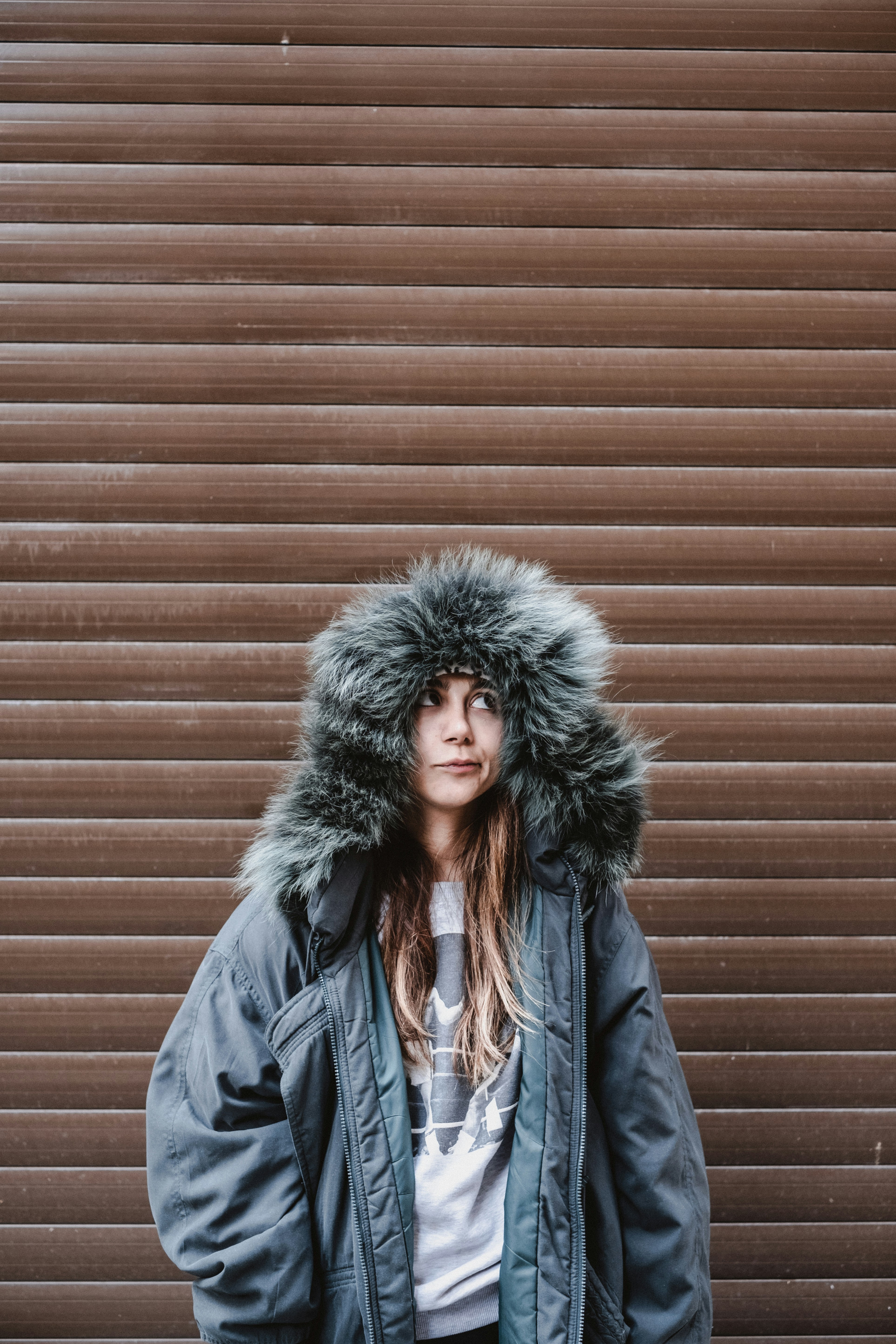 Young woman in a fur-lined hooded coat stands against a textured brown background, exuding a sense of calm amidst urban challenges.