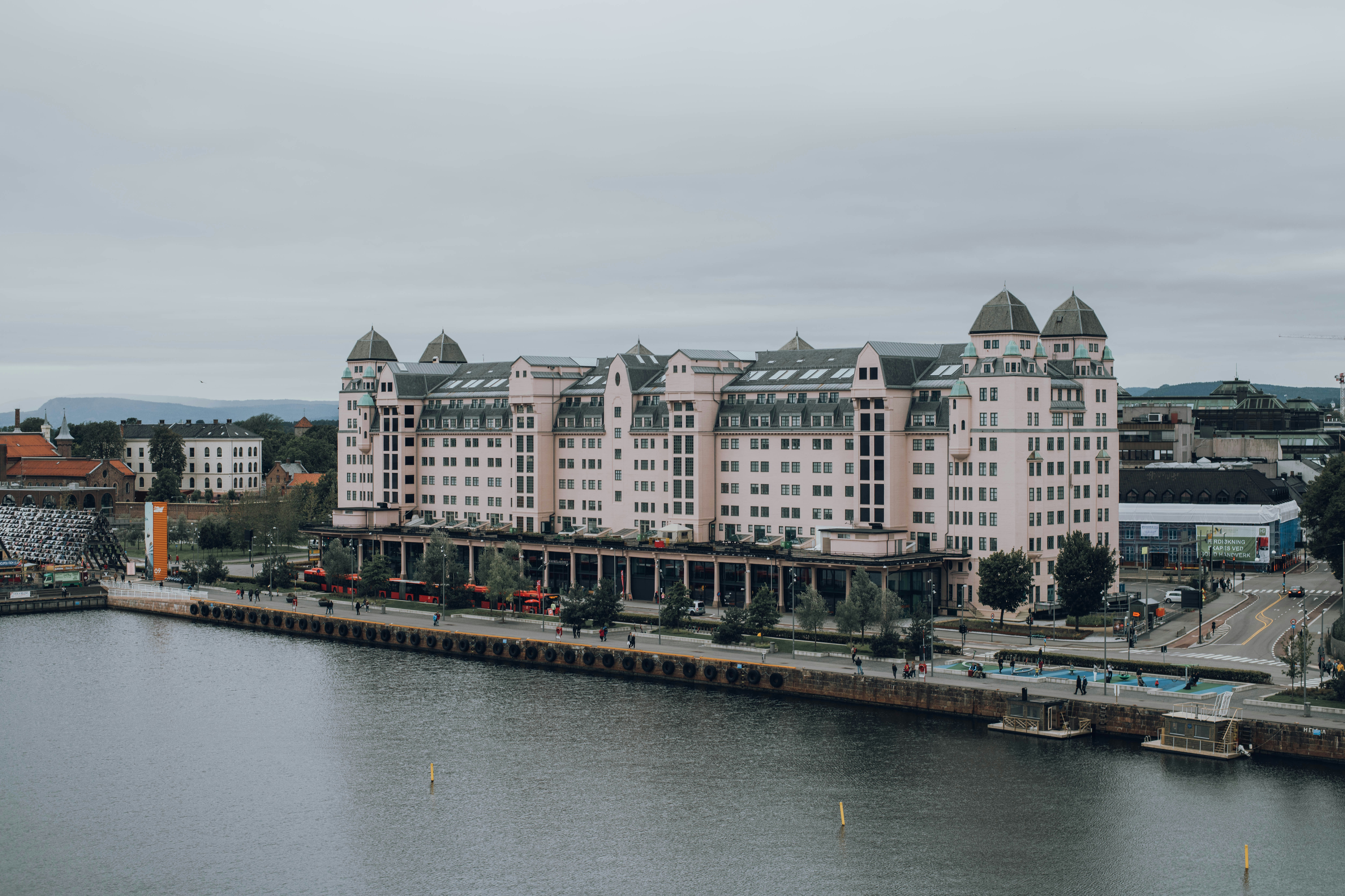 Elegant waterfront building with a distinctive pink facade, surrounded by lush greenery and calm waters.