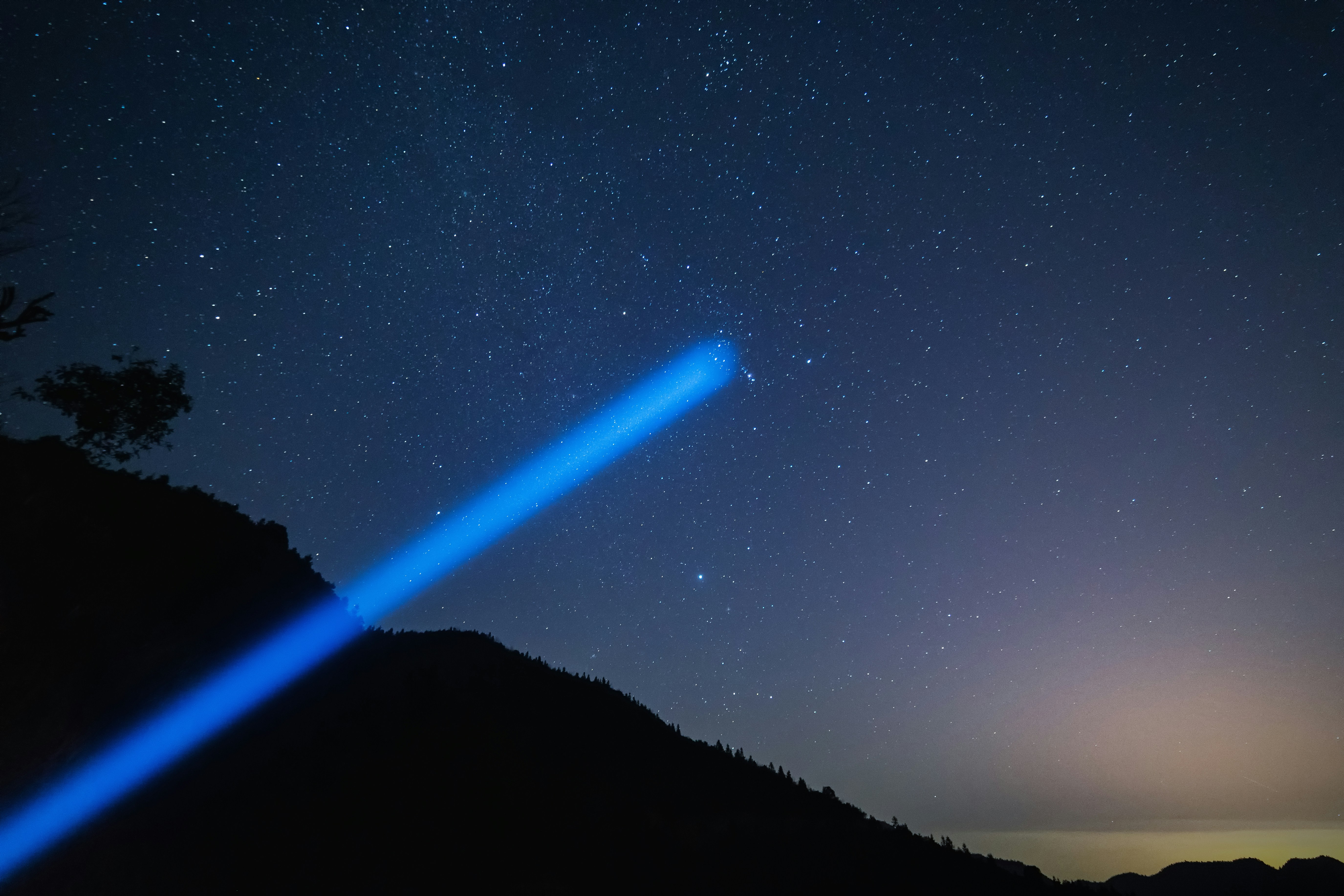 Bright blue light beam cutting through a starry night sky over a silhouetted landscape.