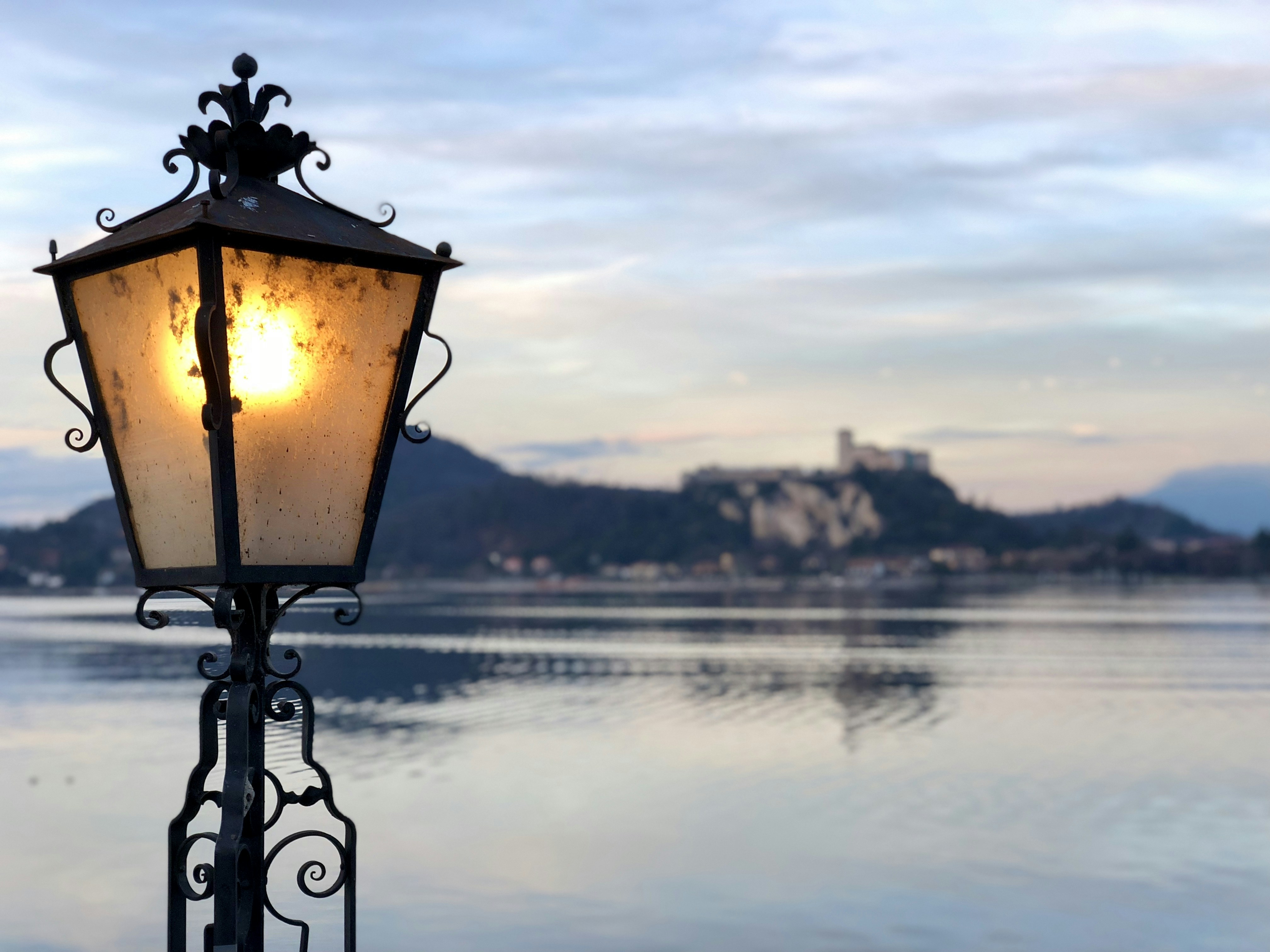 Vintage lamppost illuminating a tranquil lakeside with distant hills under a soft evening sky.