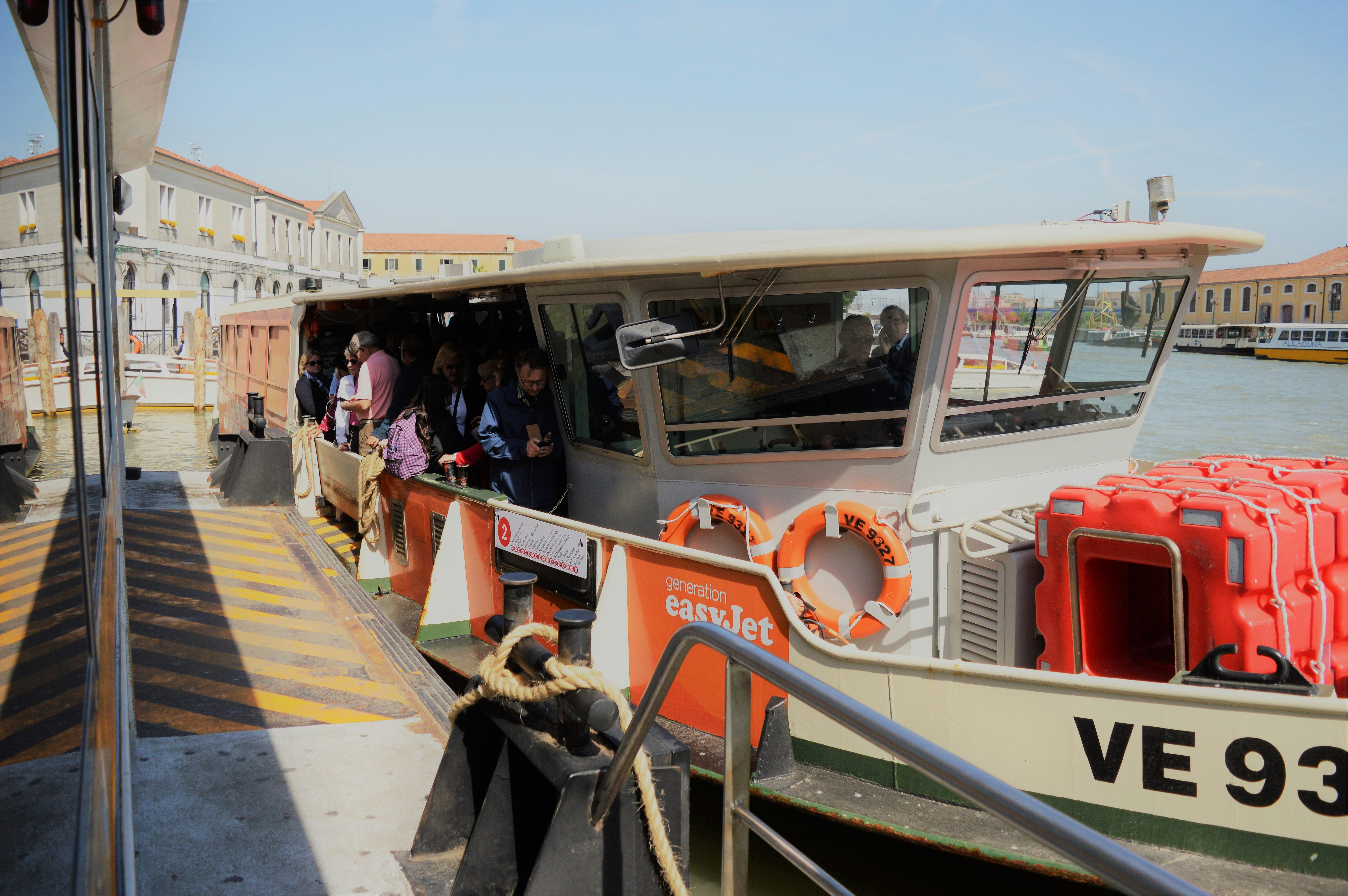 Sunlit Vaporetto at a Venetian Dock: Passengers Board Amid Colorful Canalside Architecture