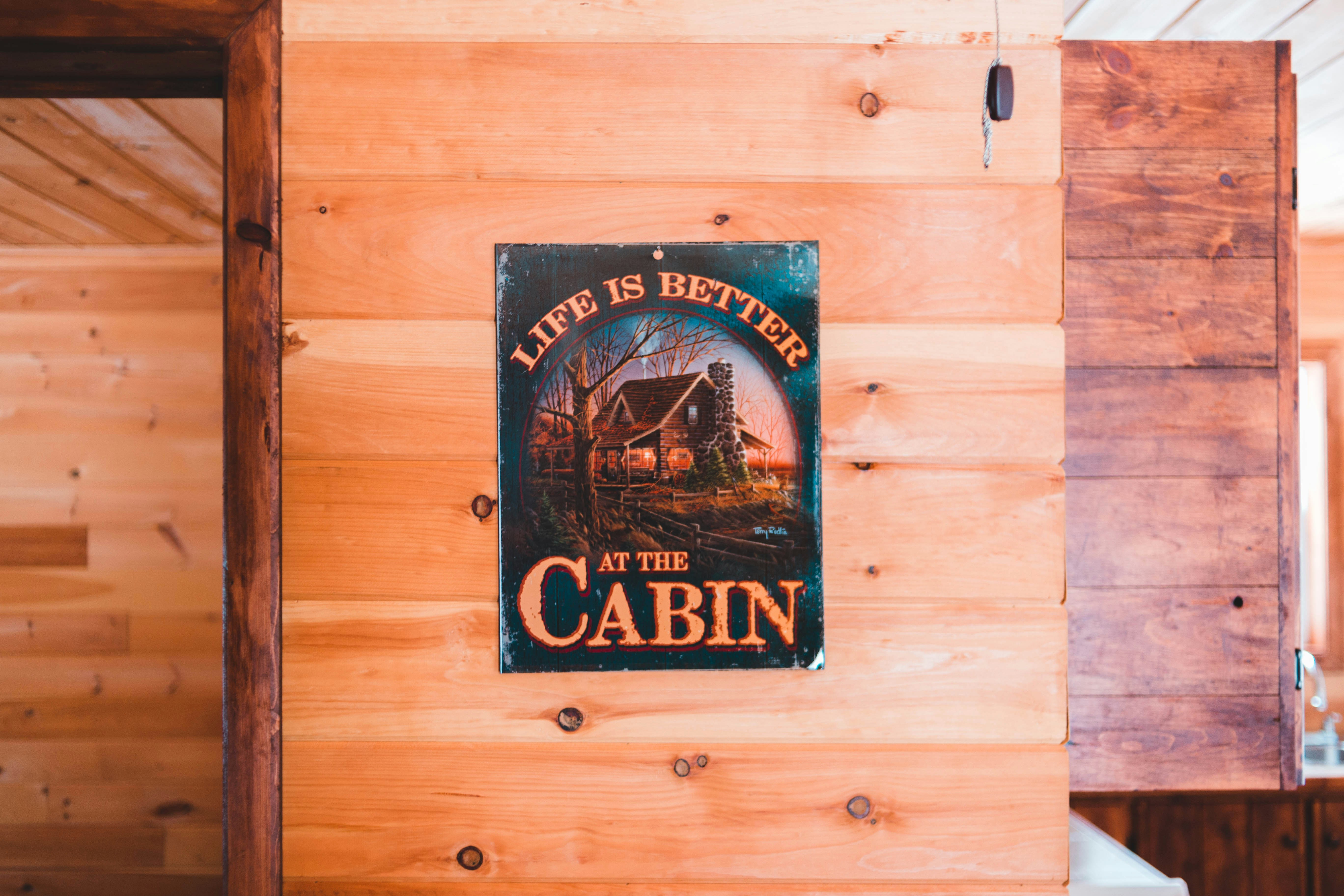 Vintage sign on a wooden wall promoting the joys of cabin life, featuring a charming illustration of a cabin.