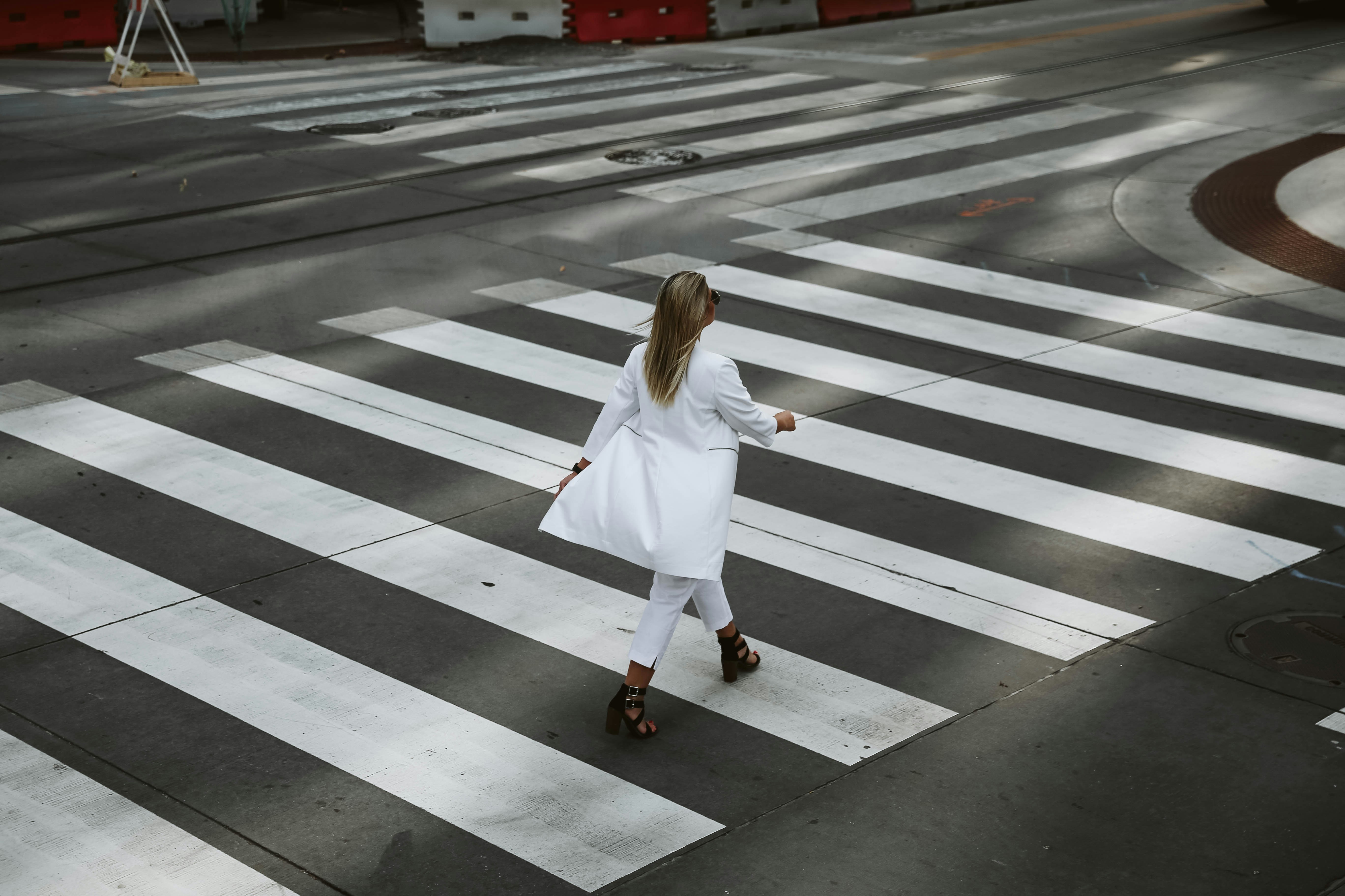 Woman in white coat walking across a striped pedestrian crosswalk.