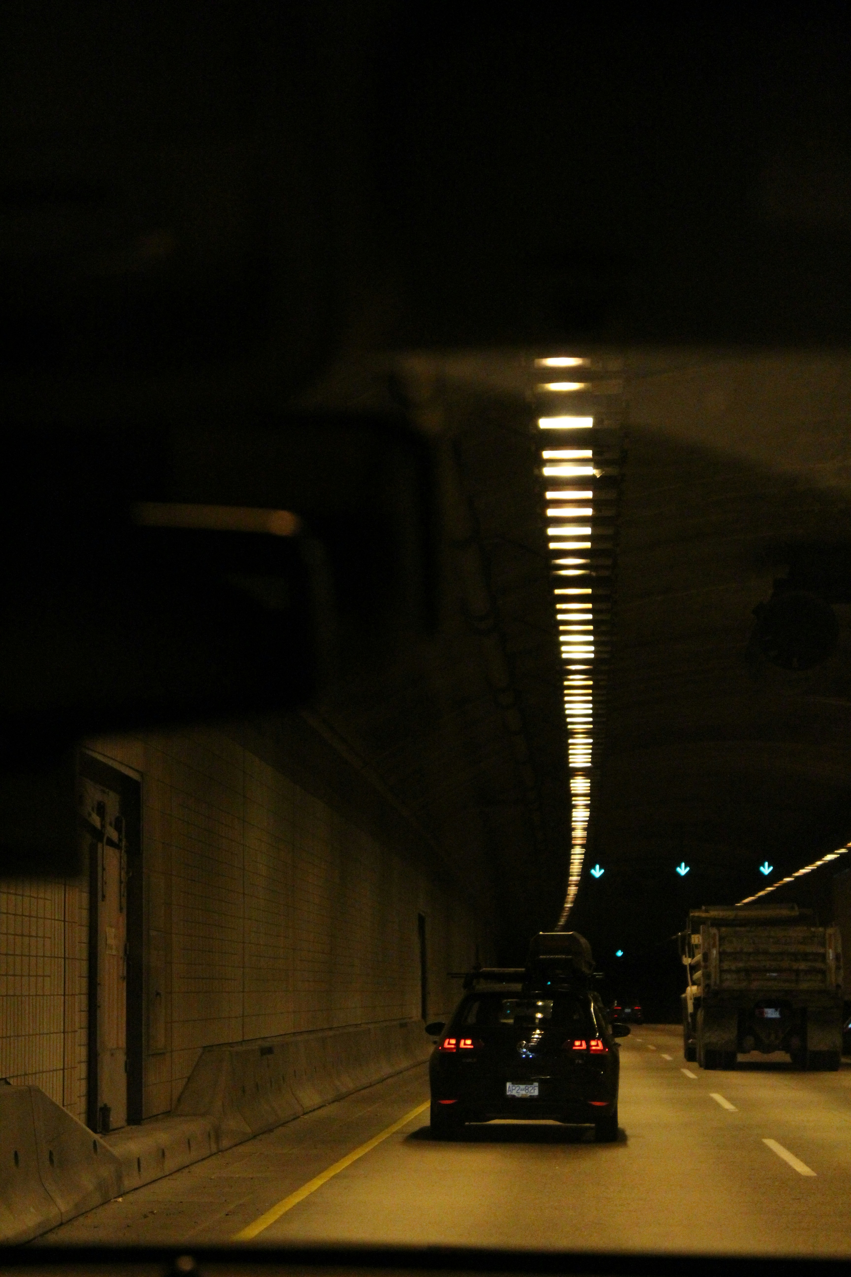 A vehicle navigating through a dimly lit tunnel, illuminated by overhead lights and traffic signals.