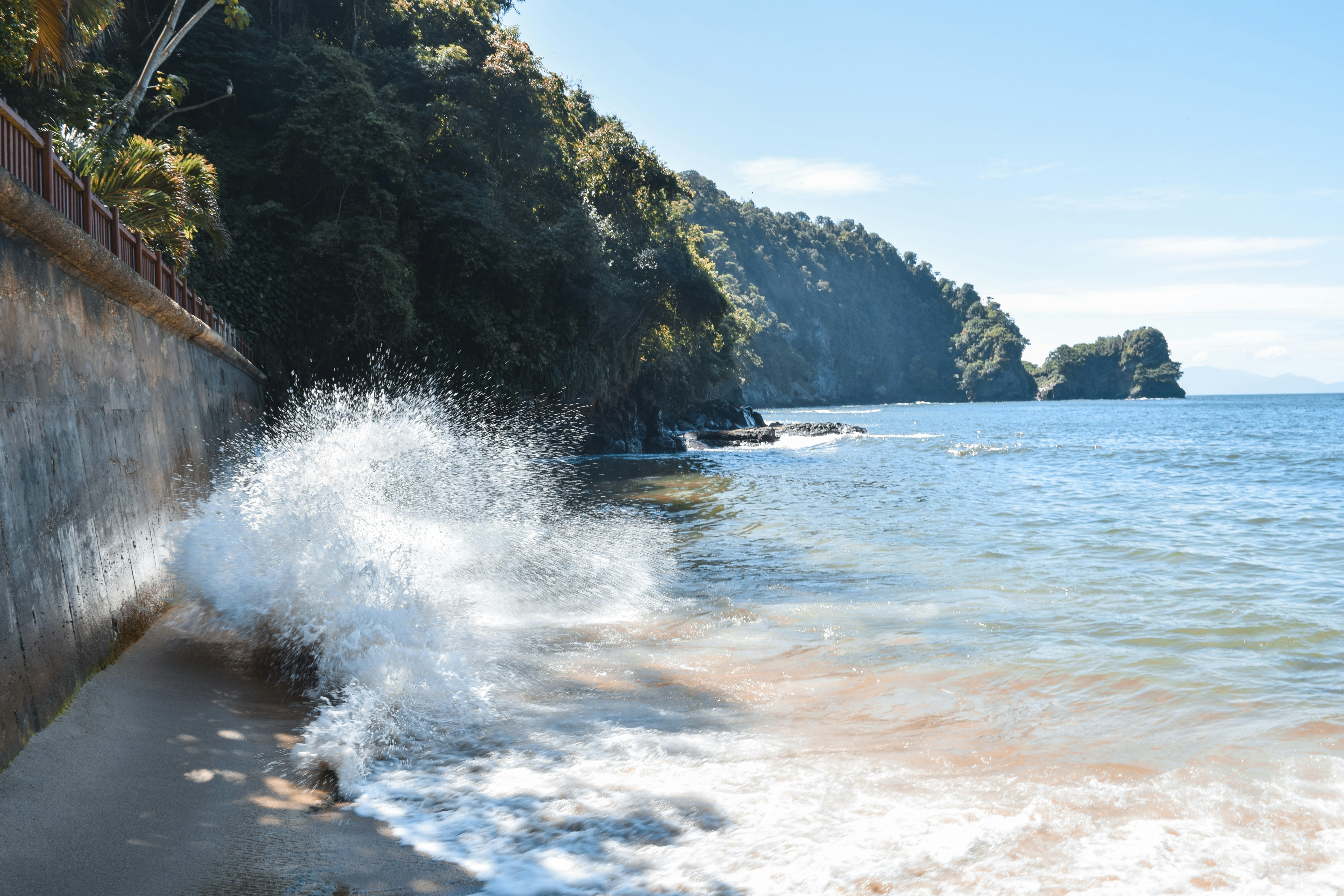 Waves crashing against a rocky coastline under a clear blue sky, showcasing the dynamic interaction between land and sea.