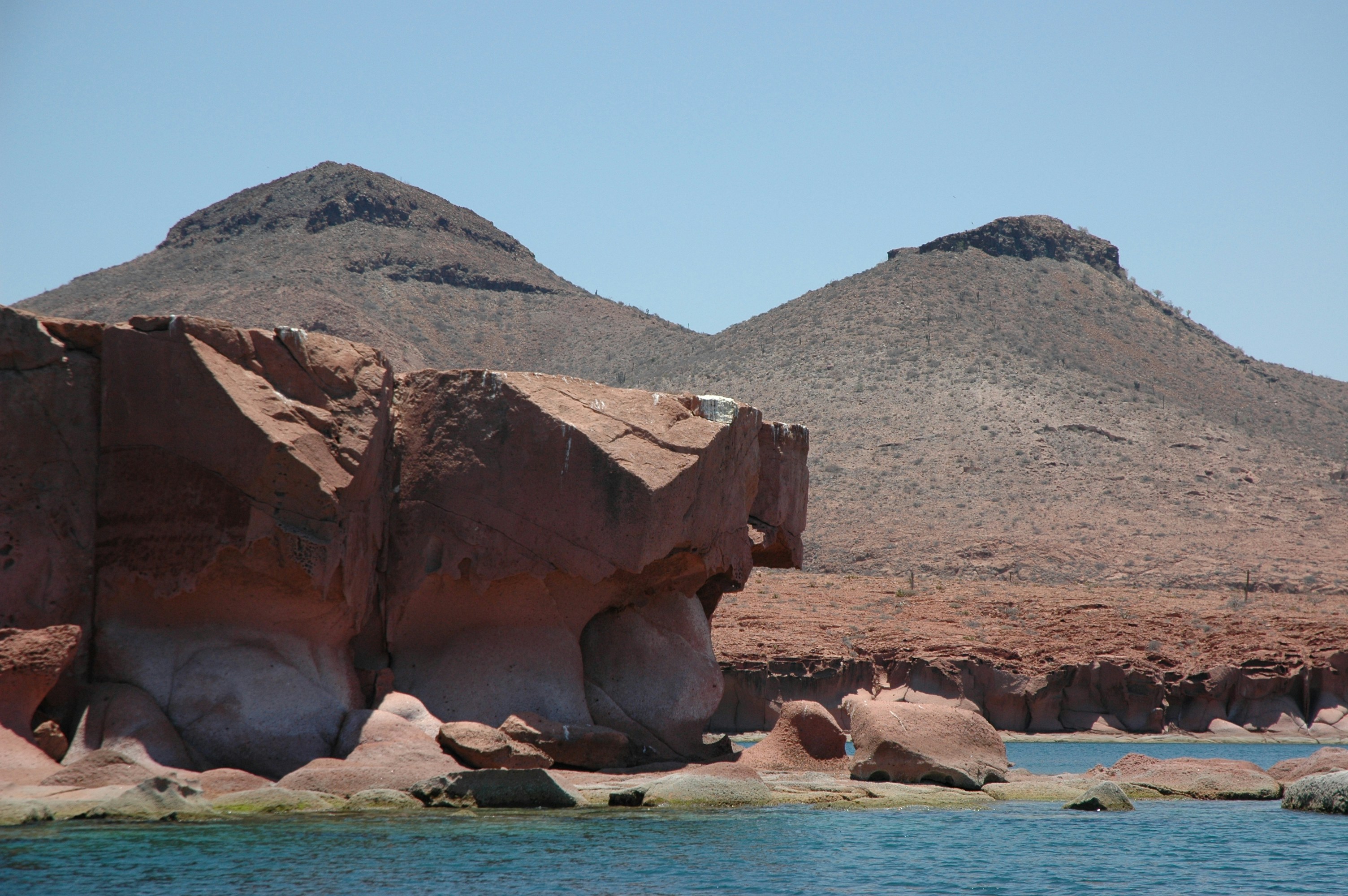 Eroded pink cliffs along a coastal landscape with calm turquoise waters under a clear sky.
