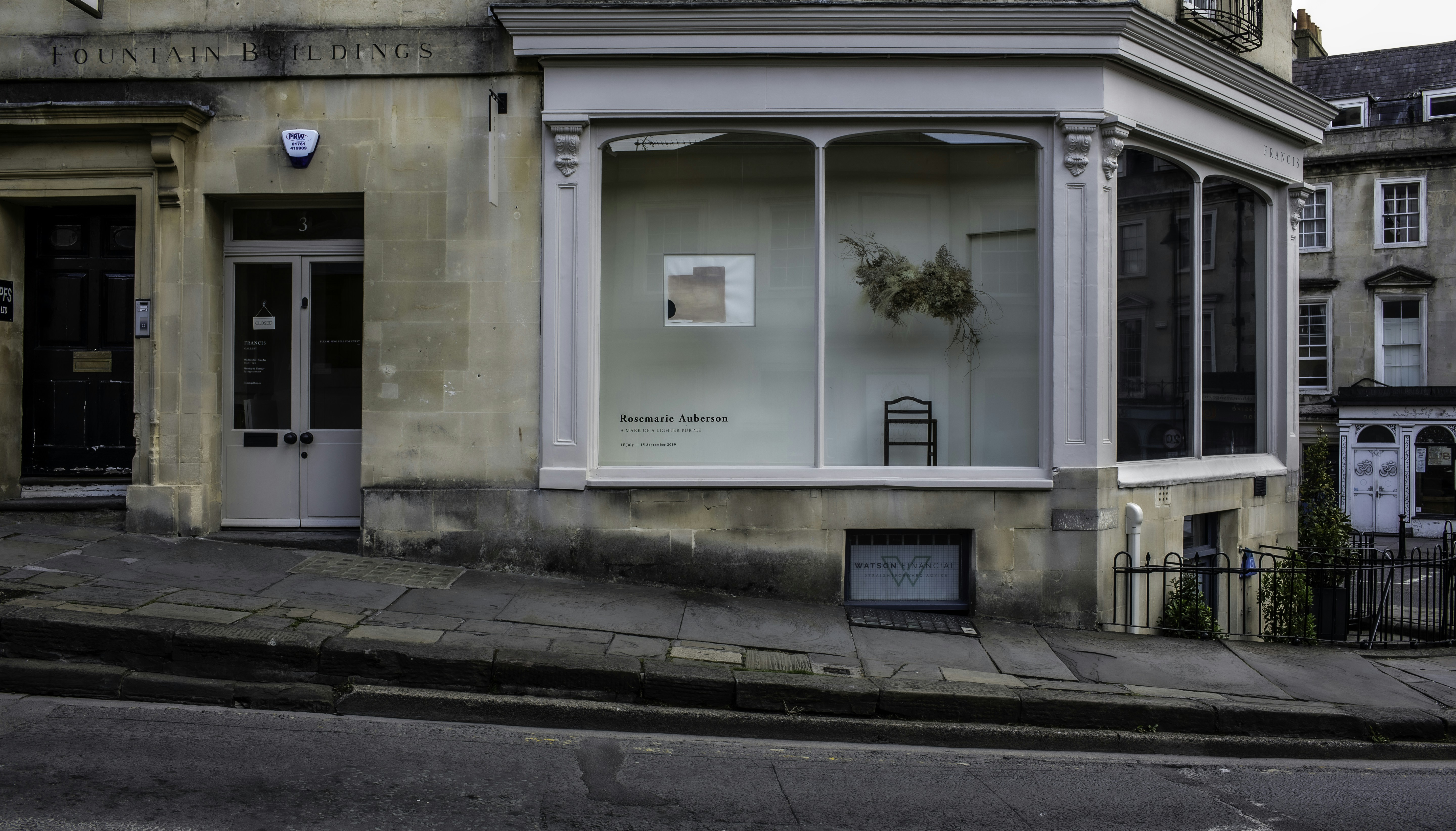 White and brown building with large windows on a sloping street.