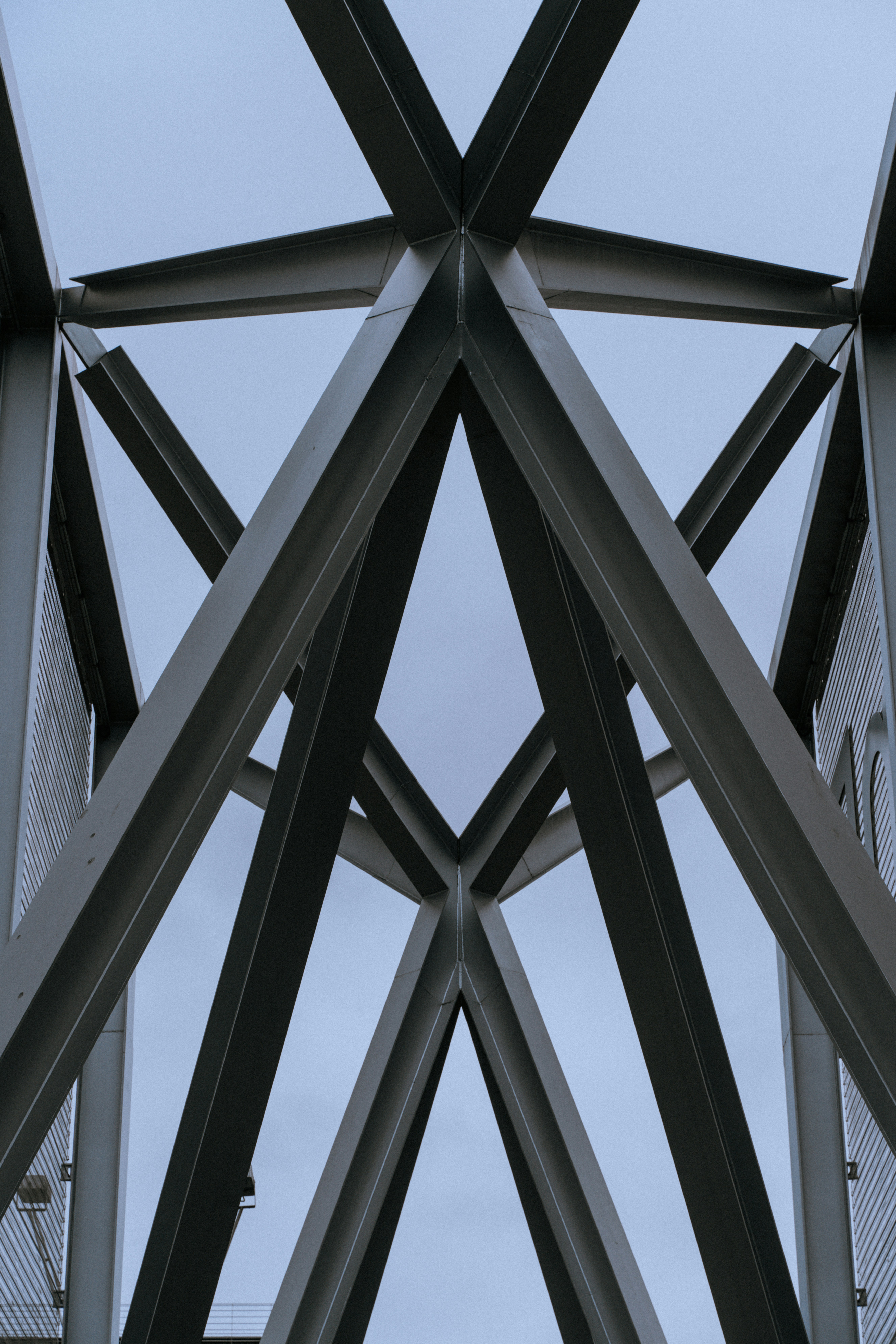 Intersecting steel beams create a striking geometric pattern against a muted sky.