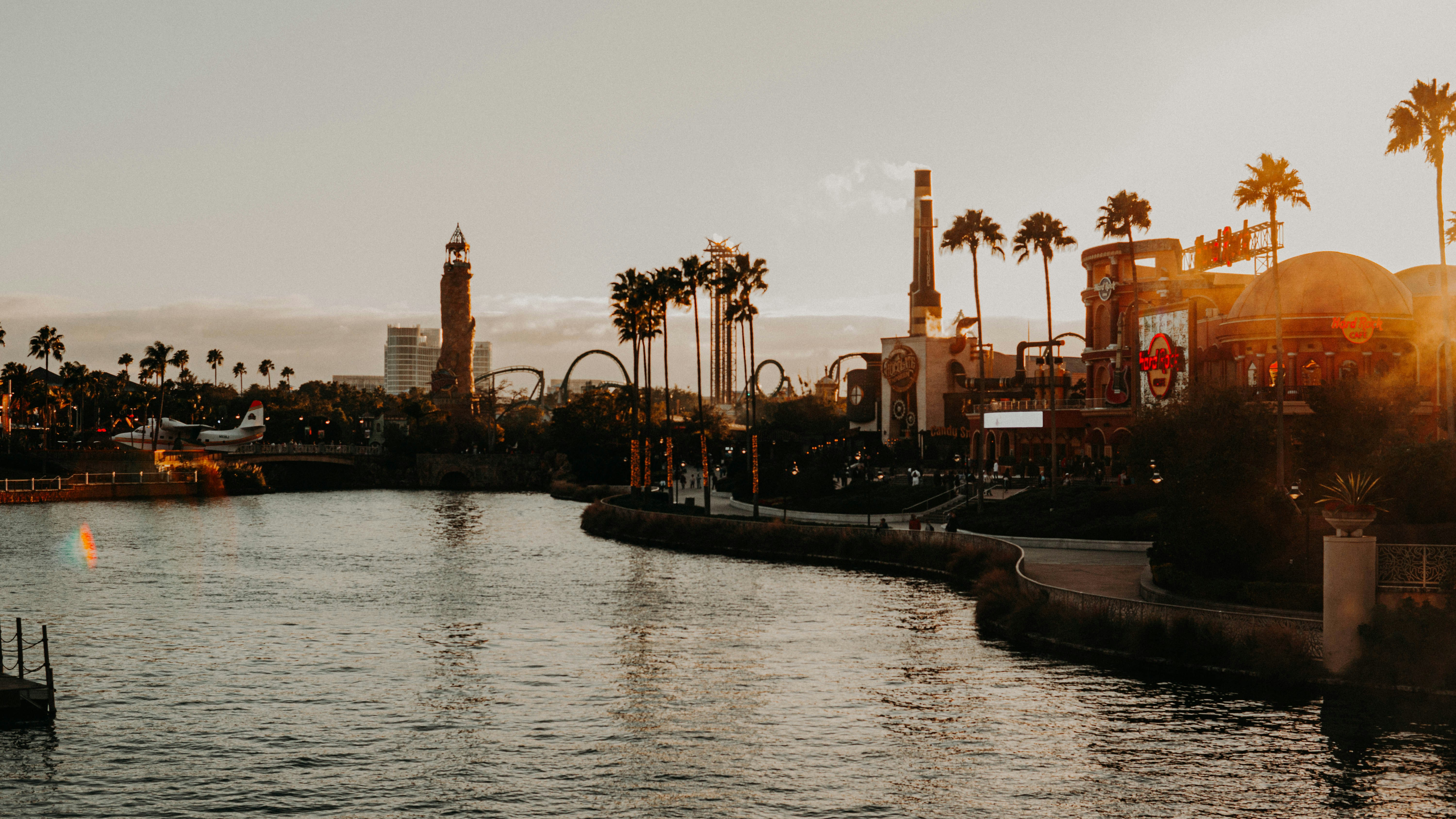 Theme park skyline reflecting in the water at dusk, framed by palm trees and warm sunlight.