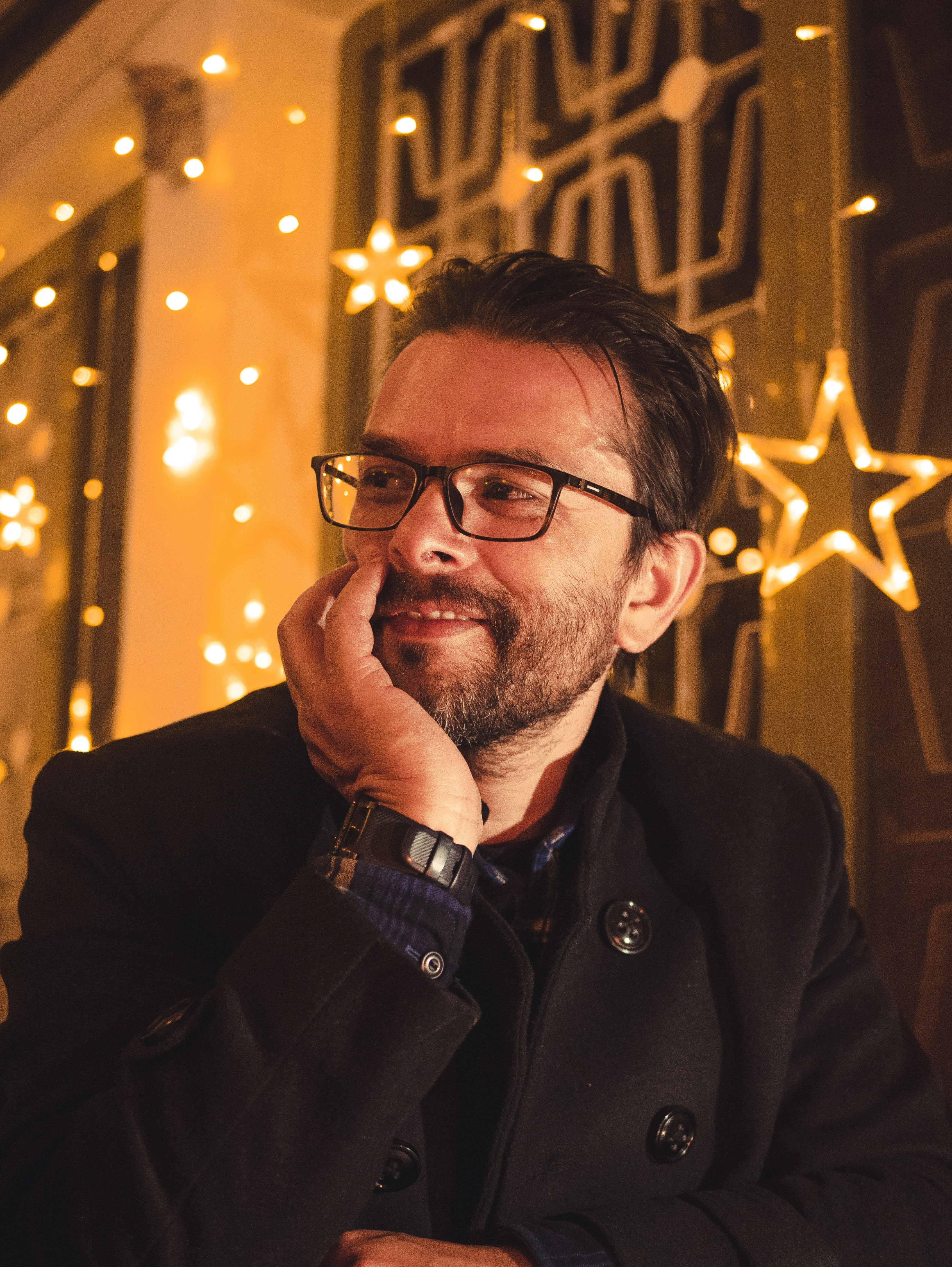Man resting his chin on his hand, surrounded by soft, glowing lights and star decorations, exuding a thoughtful demeanor.