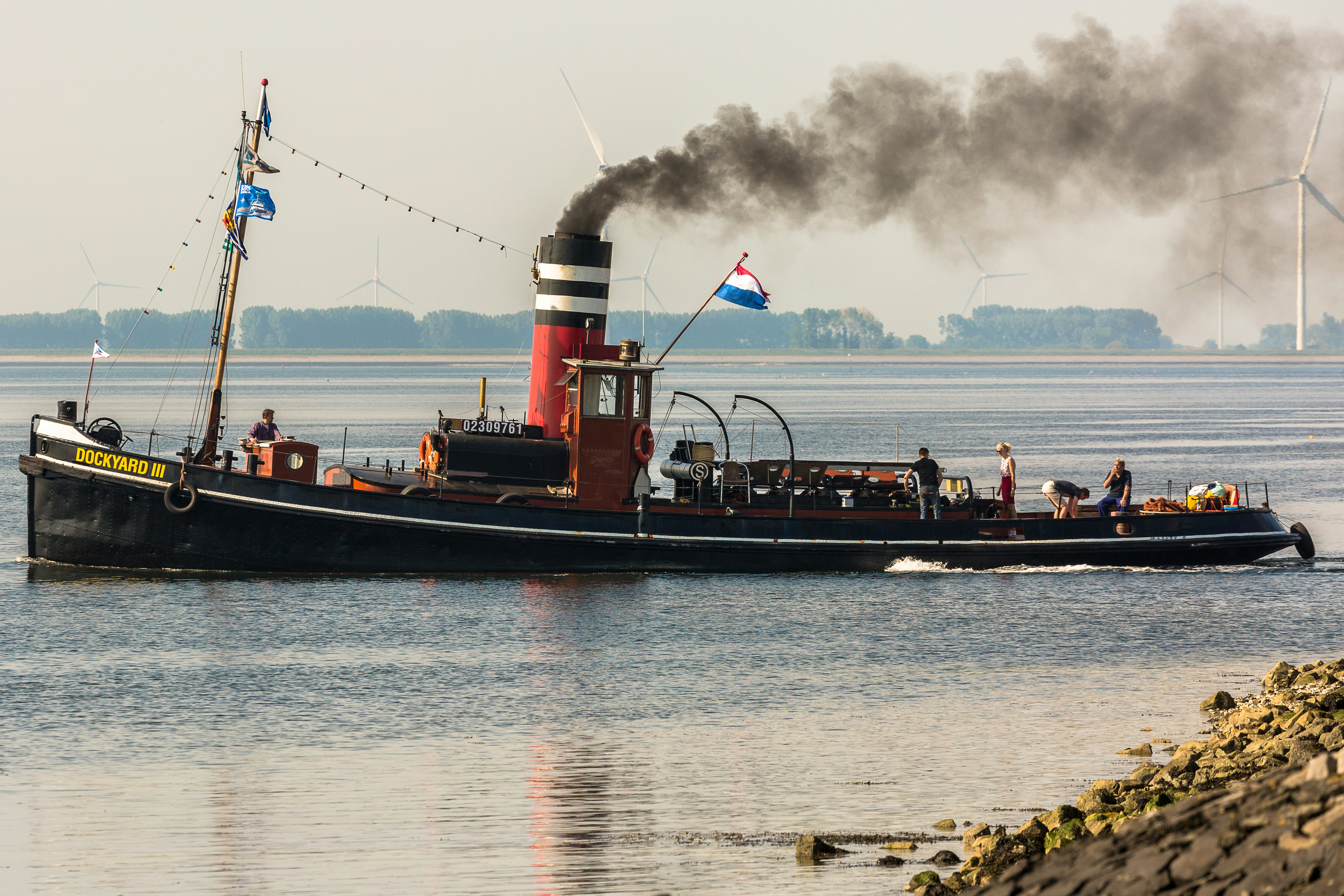 Coal-smoke Steamer Prowls a Quiet River with Distant Wind Turbines