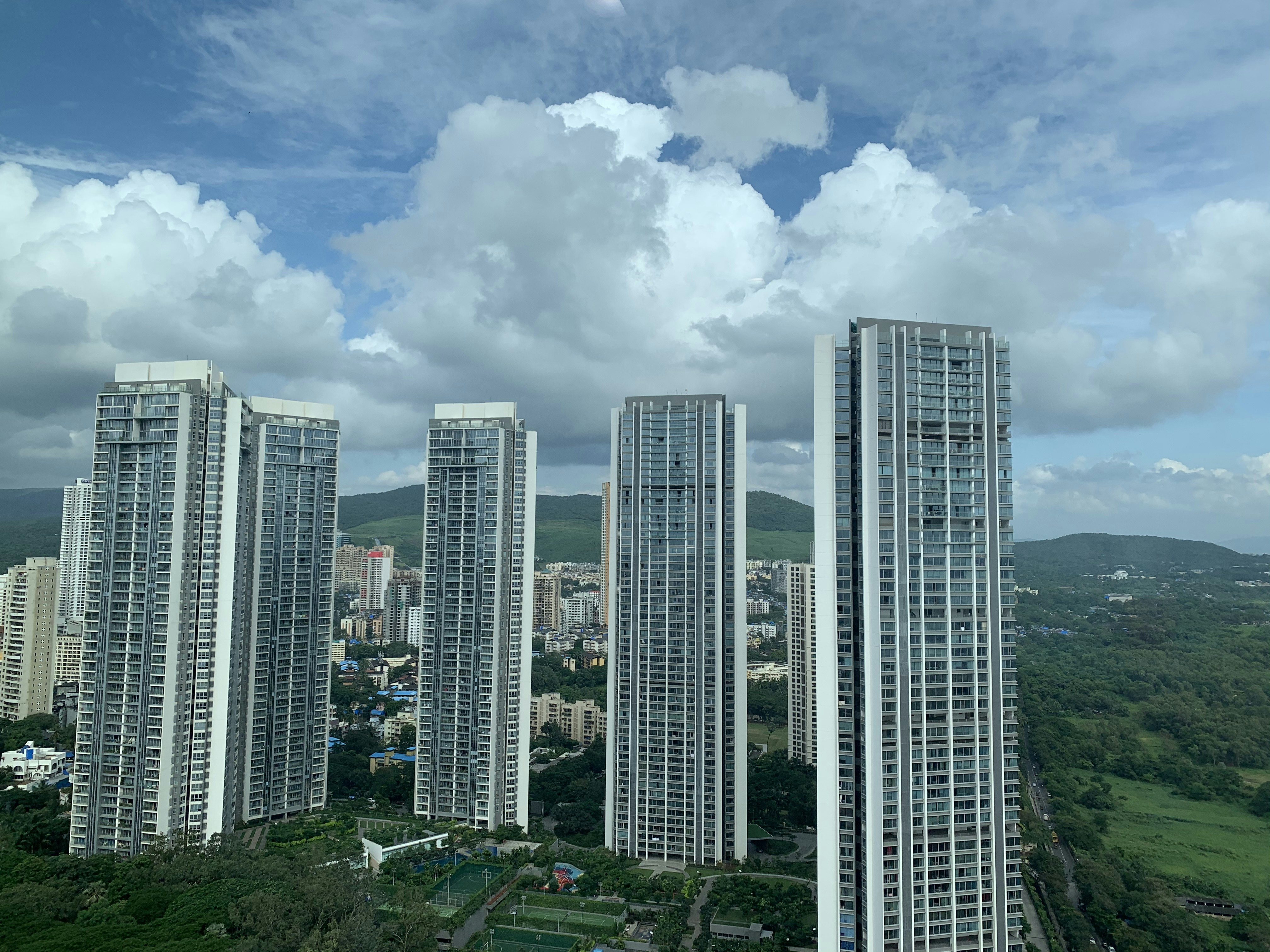 Tall skyscrapers rise against a backdrop of lush greenery and dramatic clouds.