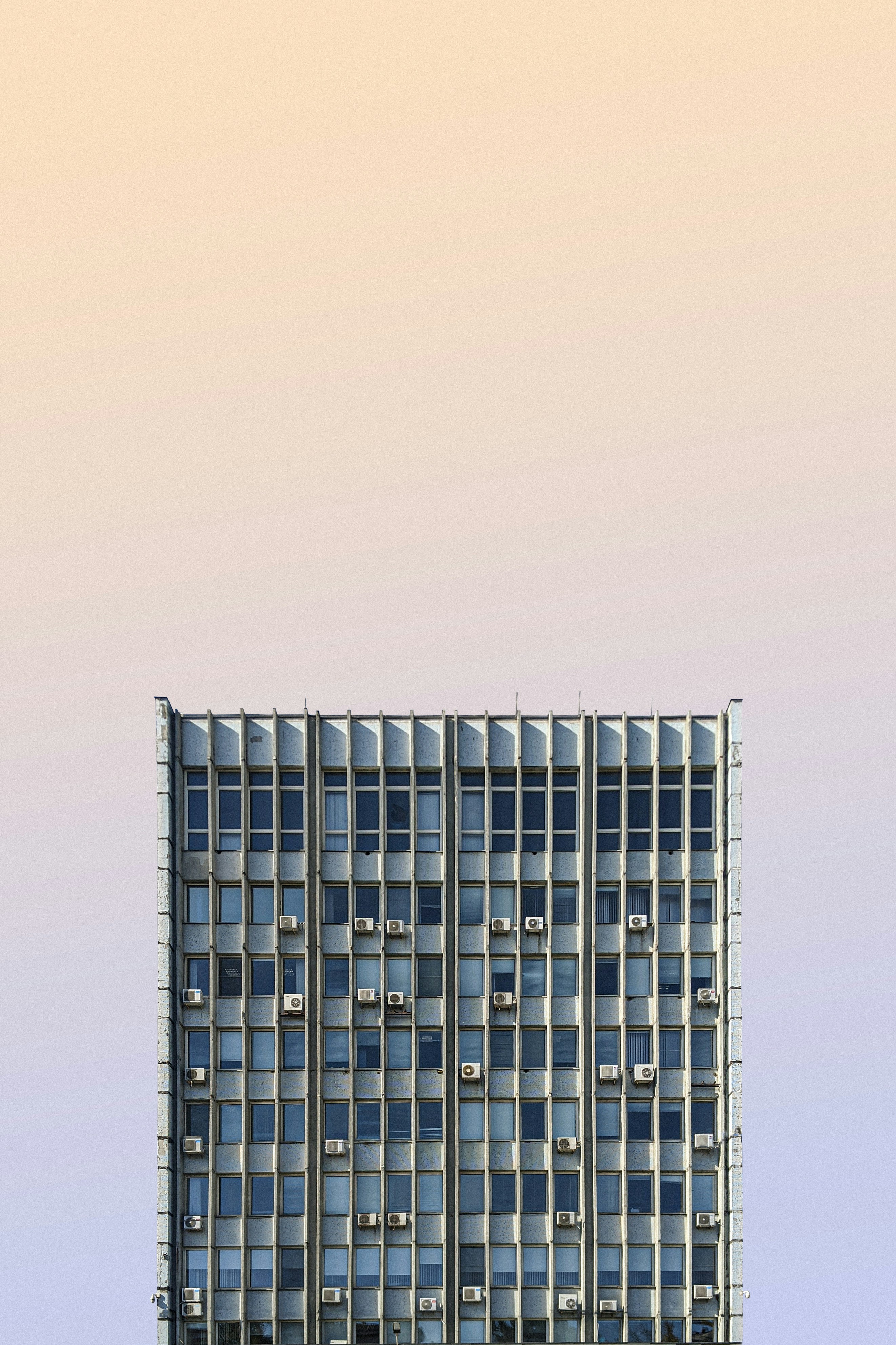 Modern office building facade adorned with numerous air conditioning units against a soft gradient sky.