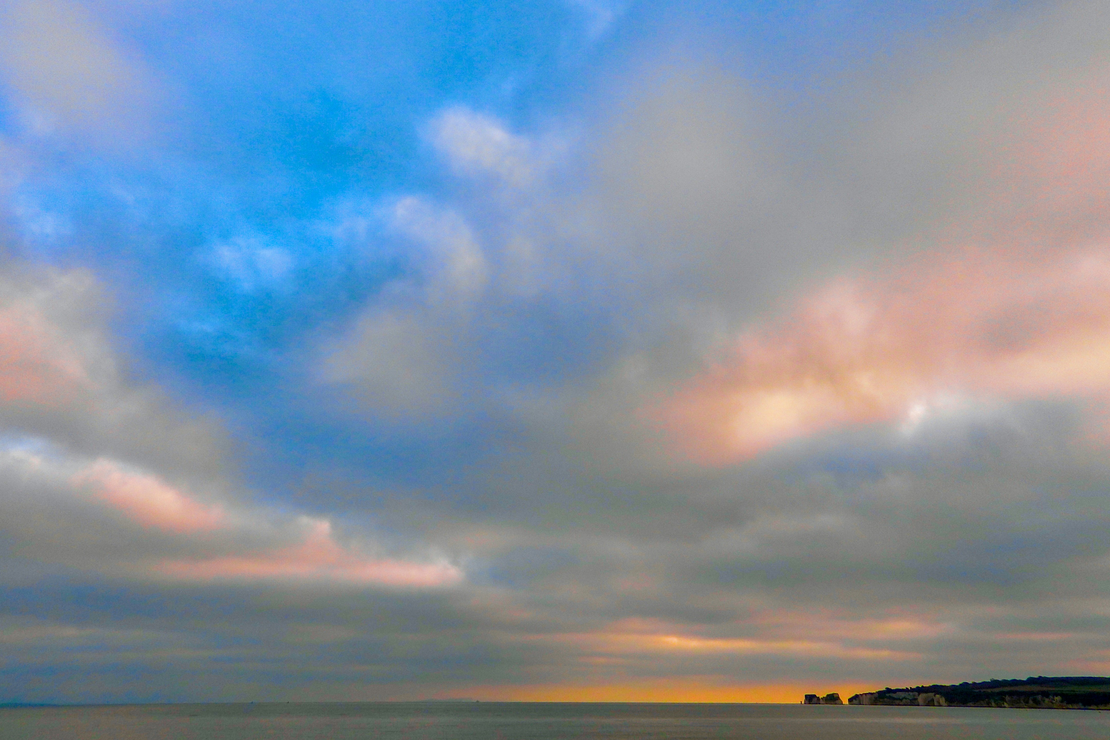 Soft pastel clouds reflect the fading light over a serene seascape, hinting at the day's end.