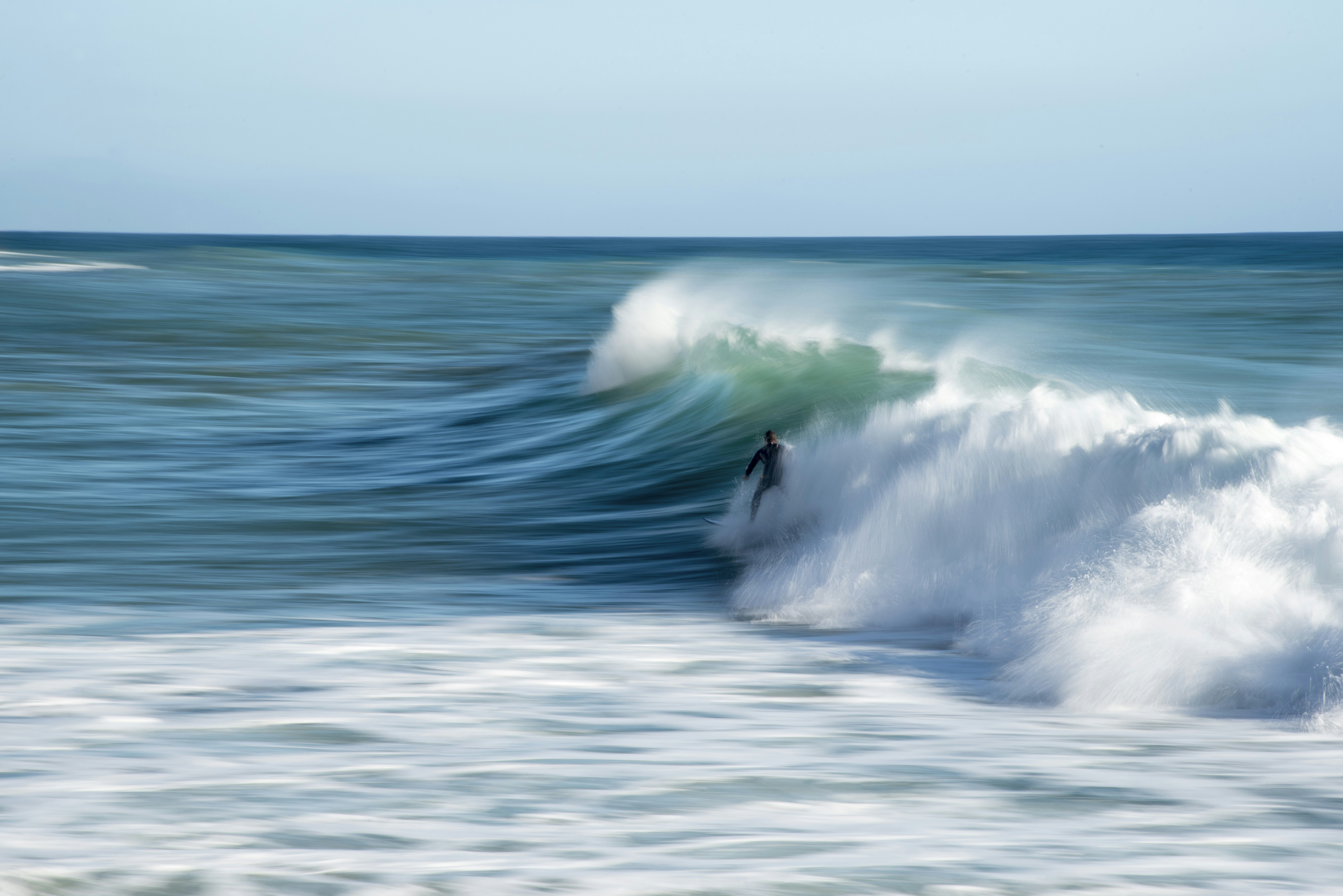 Surfer navigating a powerful ocean wave under a clear blue sky.