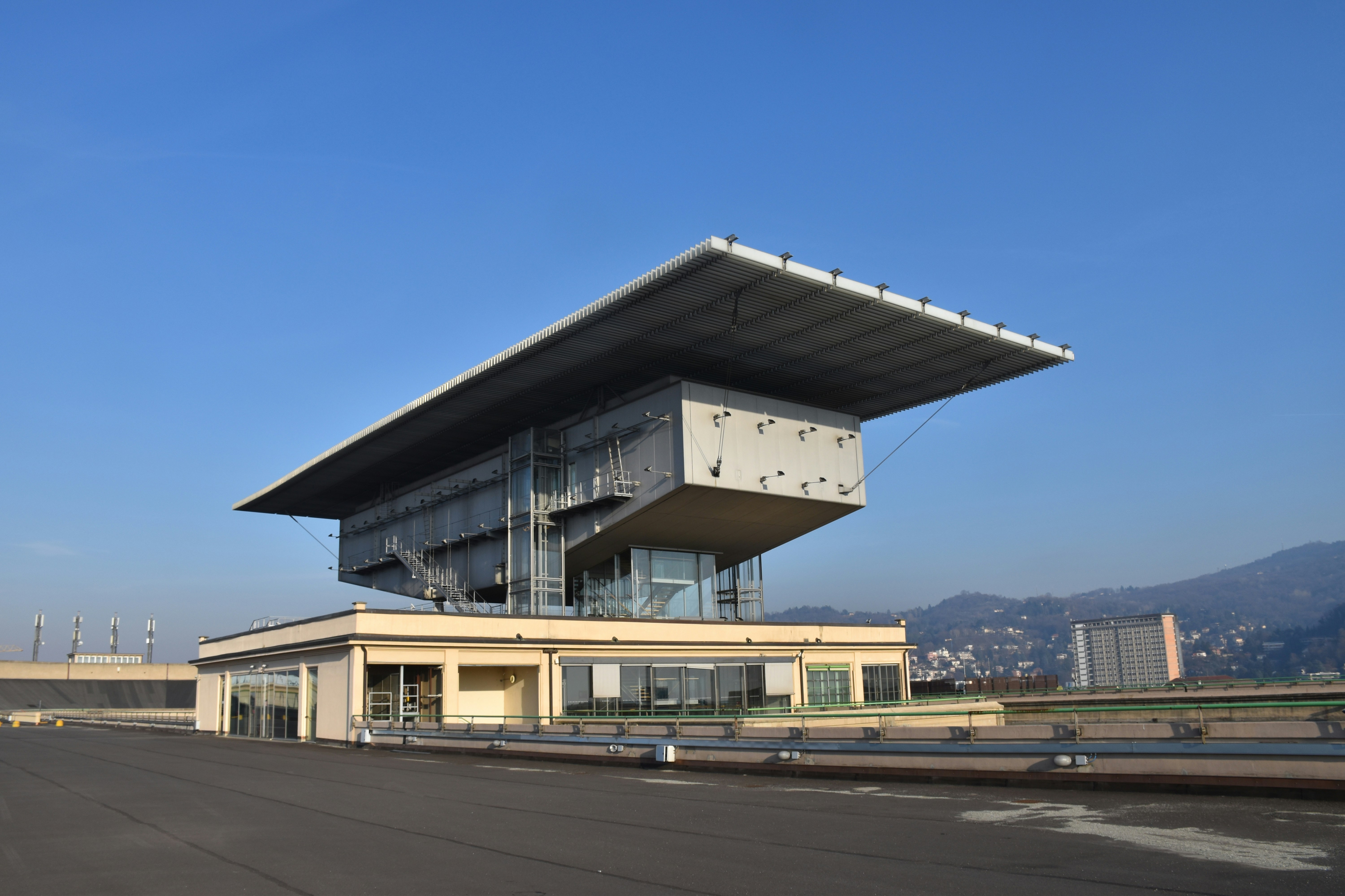 Modern glass structure atop the historic Fiat factory in Turin under clear blue skies.