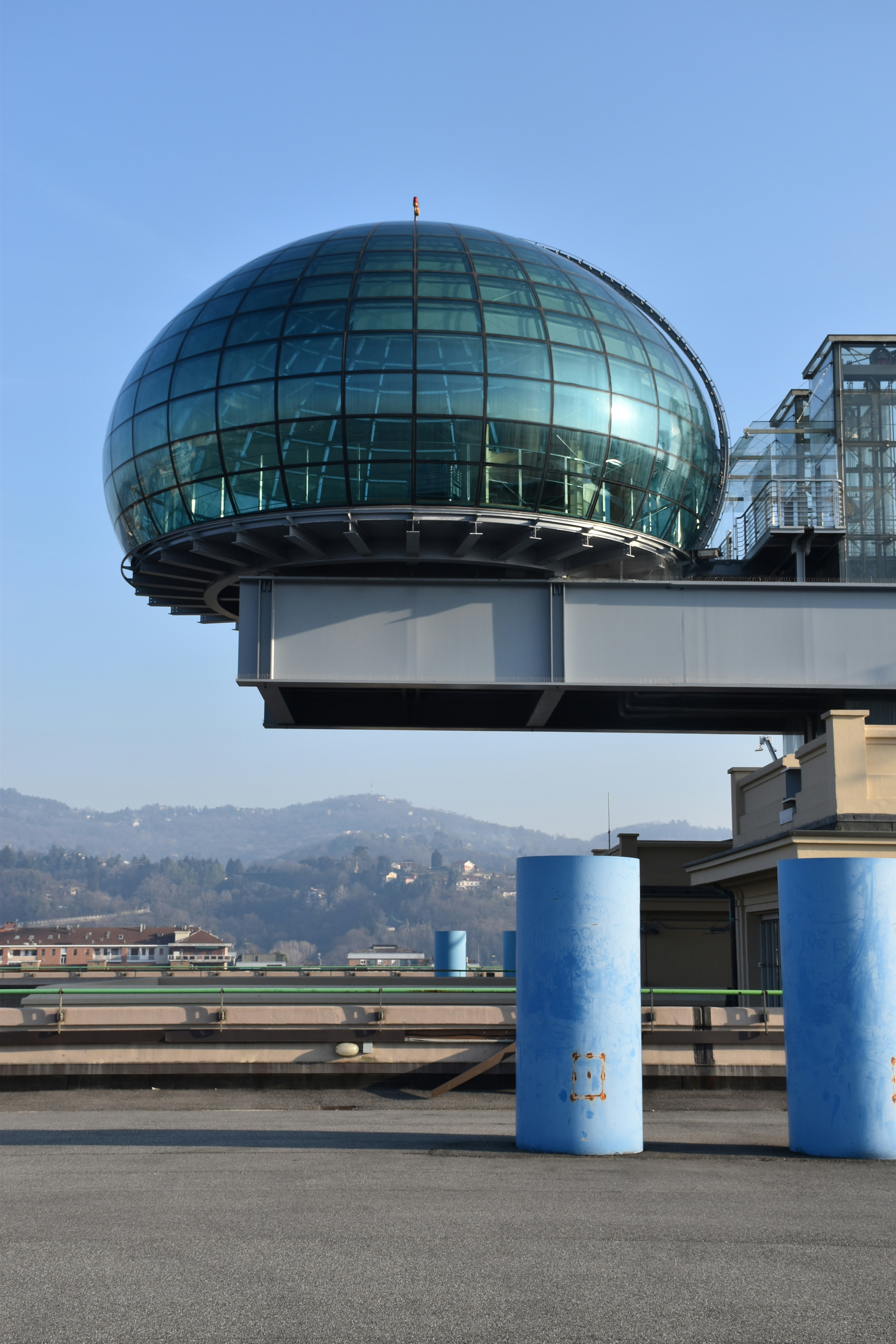 A futuristic glass dome structure suspended above a rooftop, showcasing innovative design against a clear blue sky.