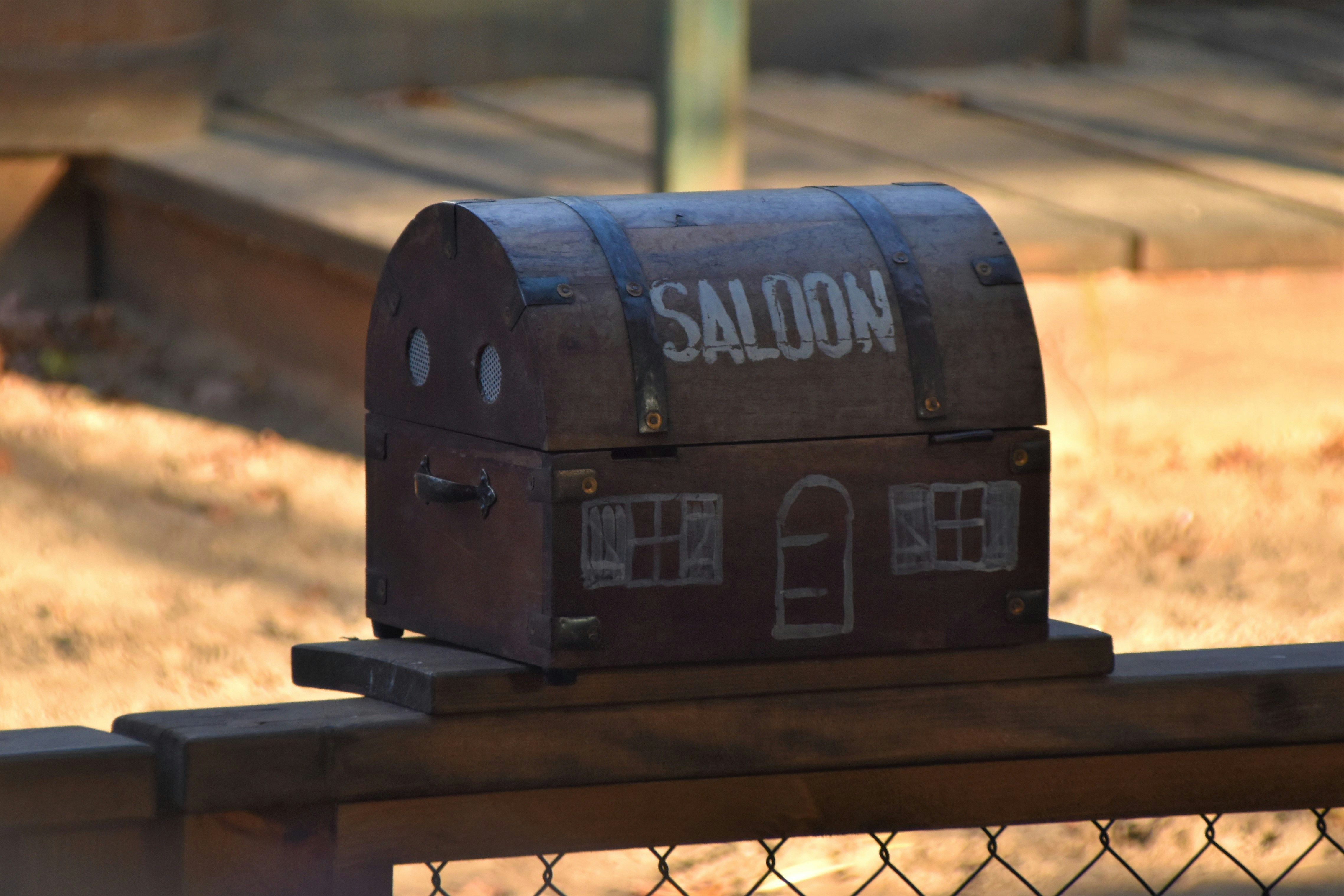 Wooden saloon-style box with painted details, positioned on a fence in a rustic setting.