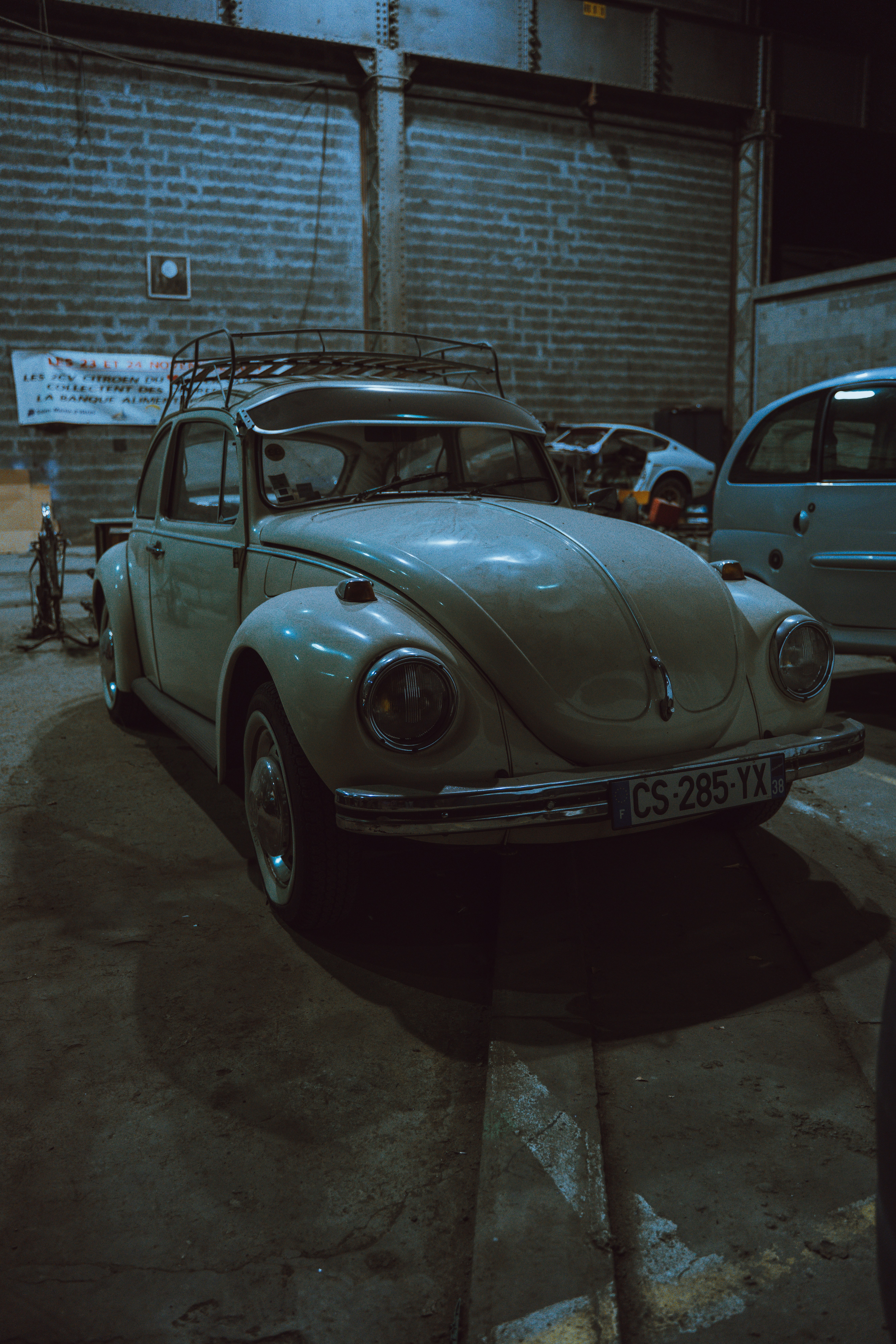 Vintage Volkswagen Beetle parked in a dimly lit garage, showcasing its timeless design amidst industrial surroundings.