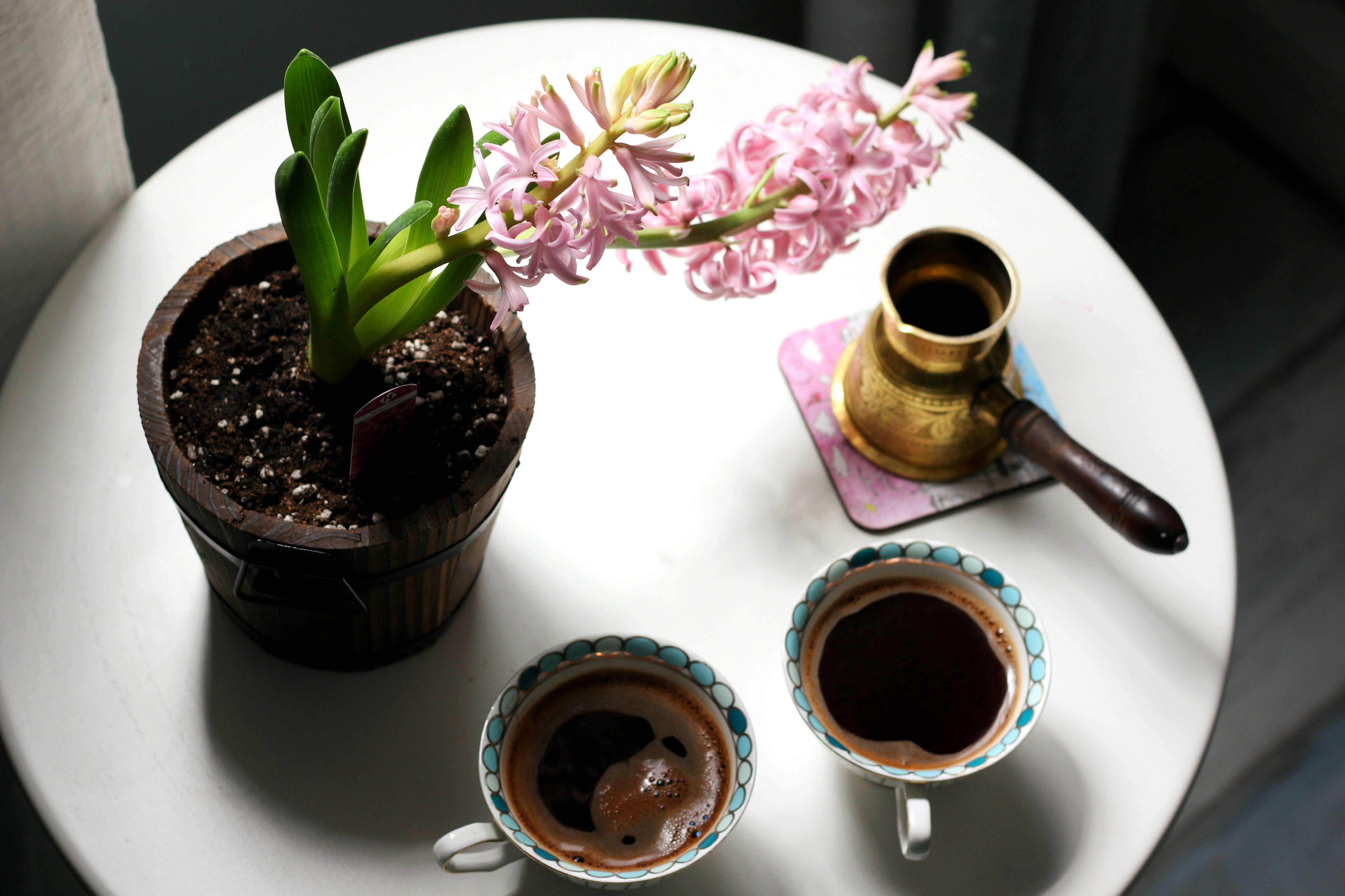 A cozy scene featuring two cups of coffee beside a blooming hyacinth plant and a traditional coffee pot on a round table.