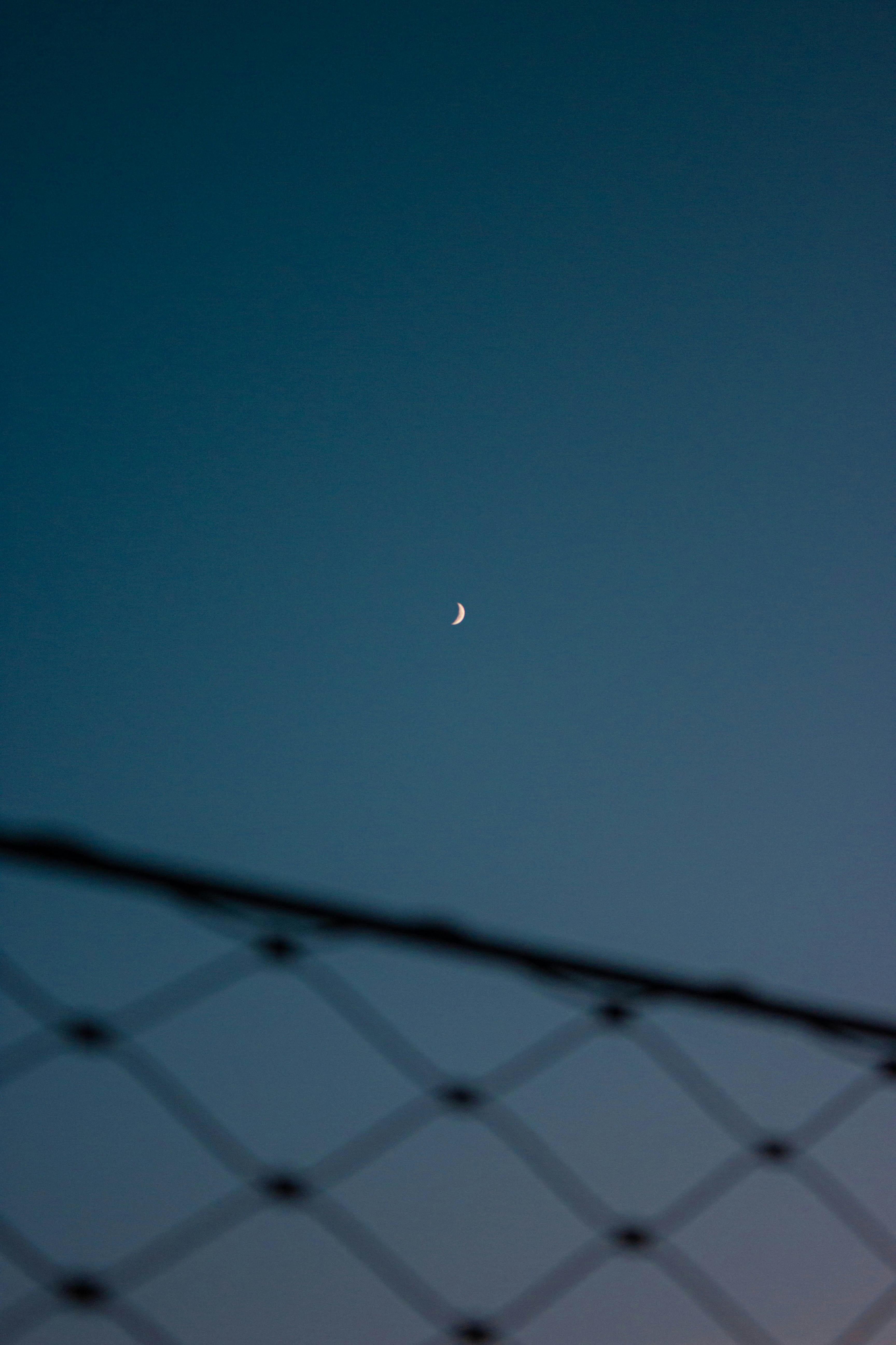 Moonlit Mesh: Crescent Moon Above a Dim Fenced Horizon