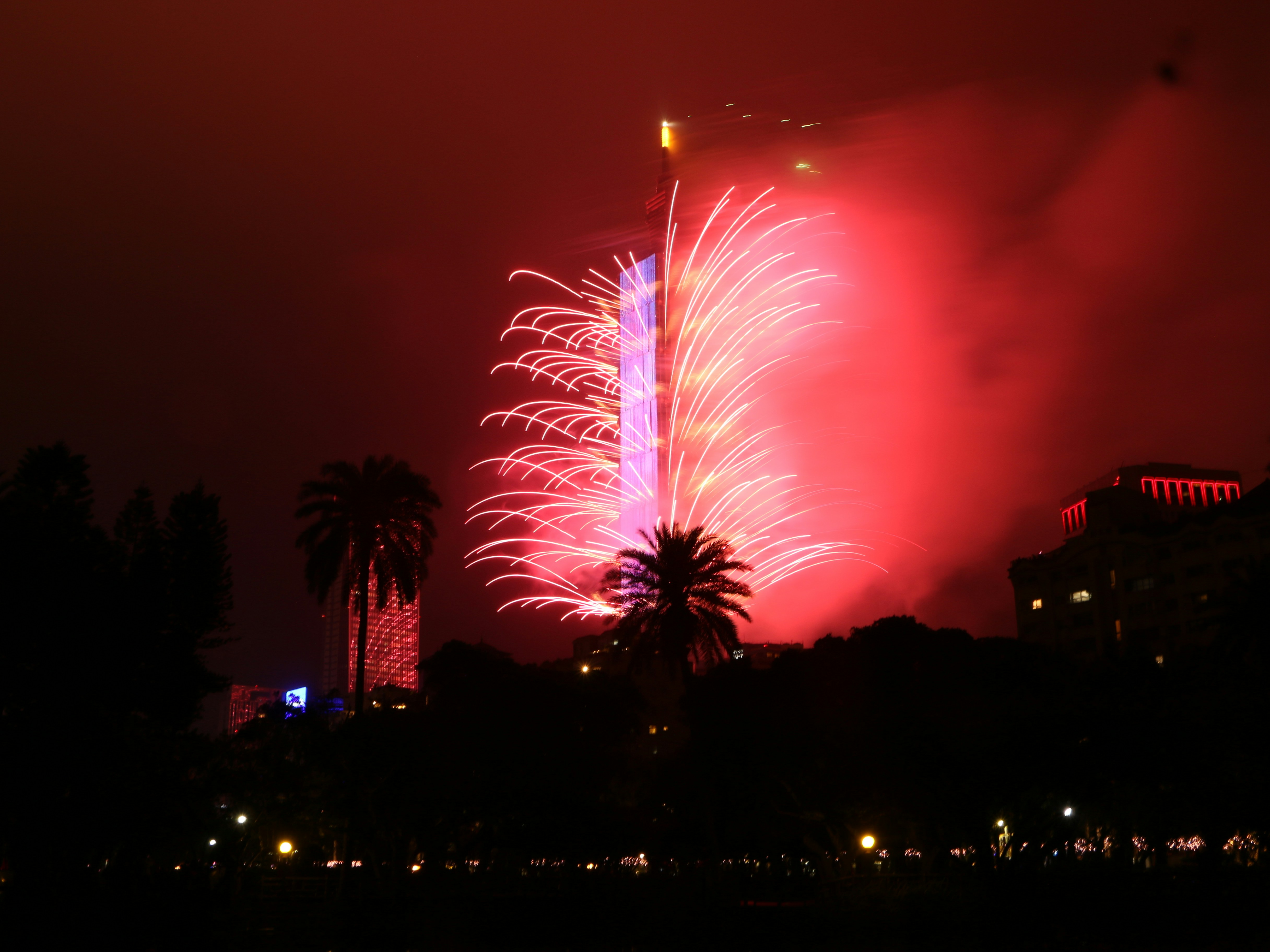 Crimson Neon Tower Sparks Over a Palm-Fringed Night Skyline