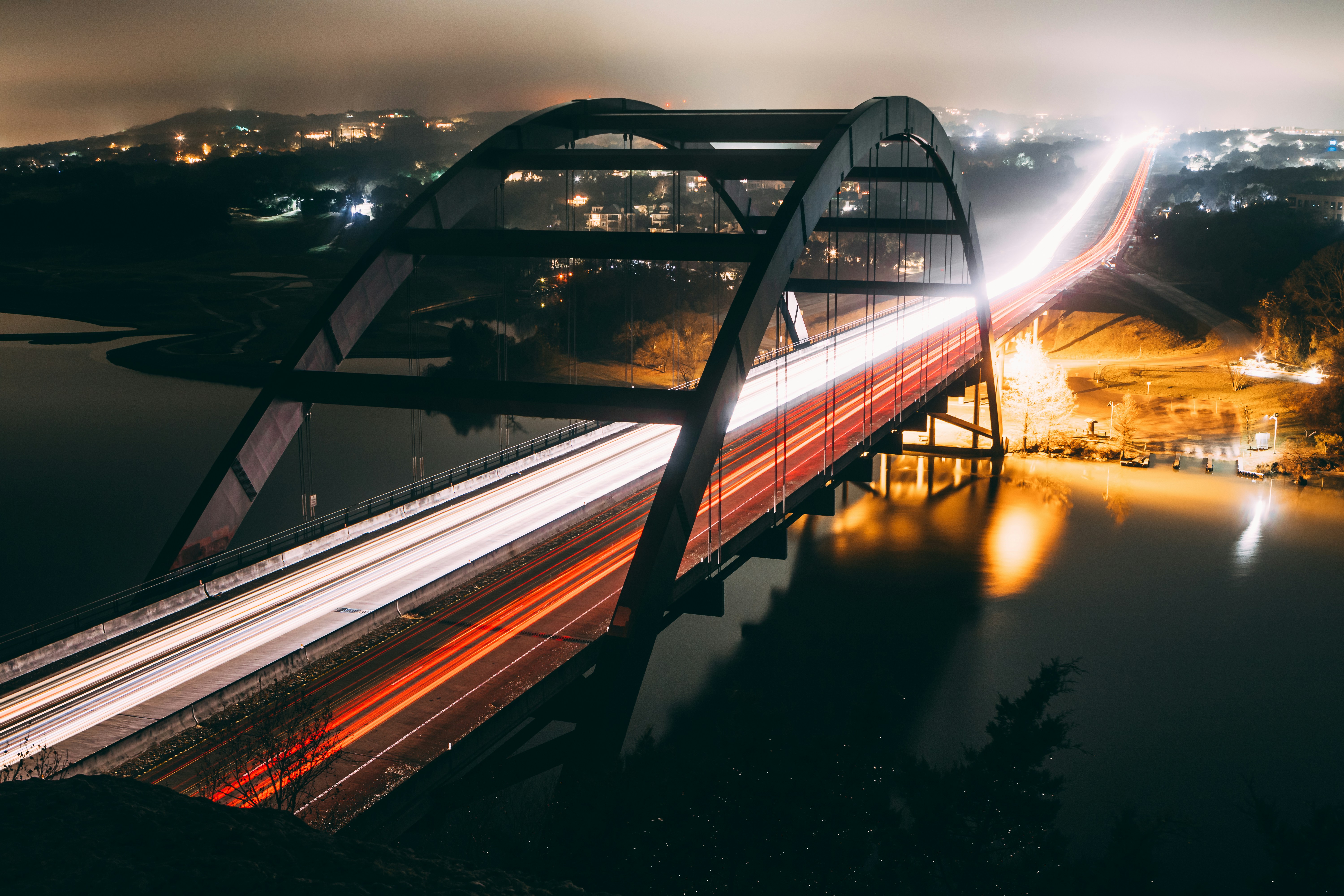 Long exposure of cars creating light trails on an arched bridge at night.