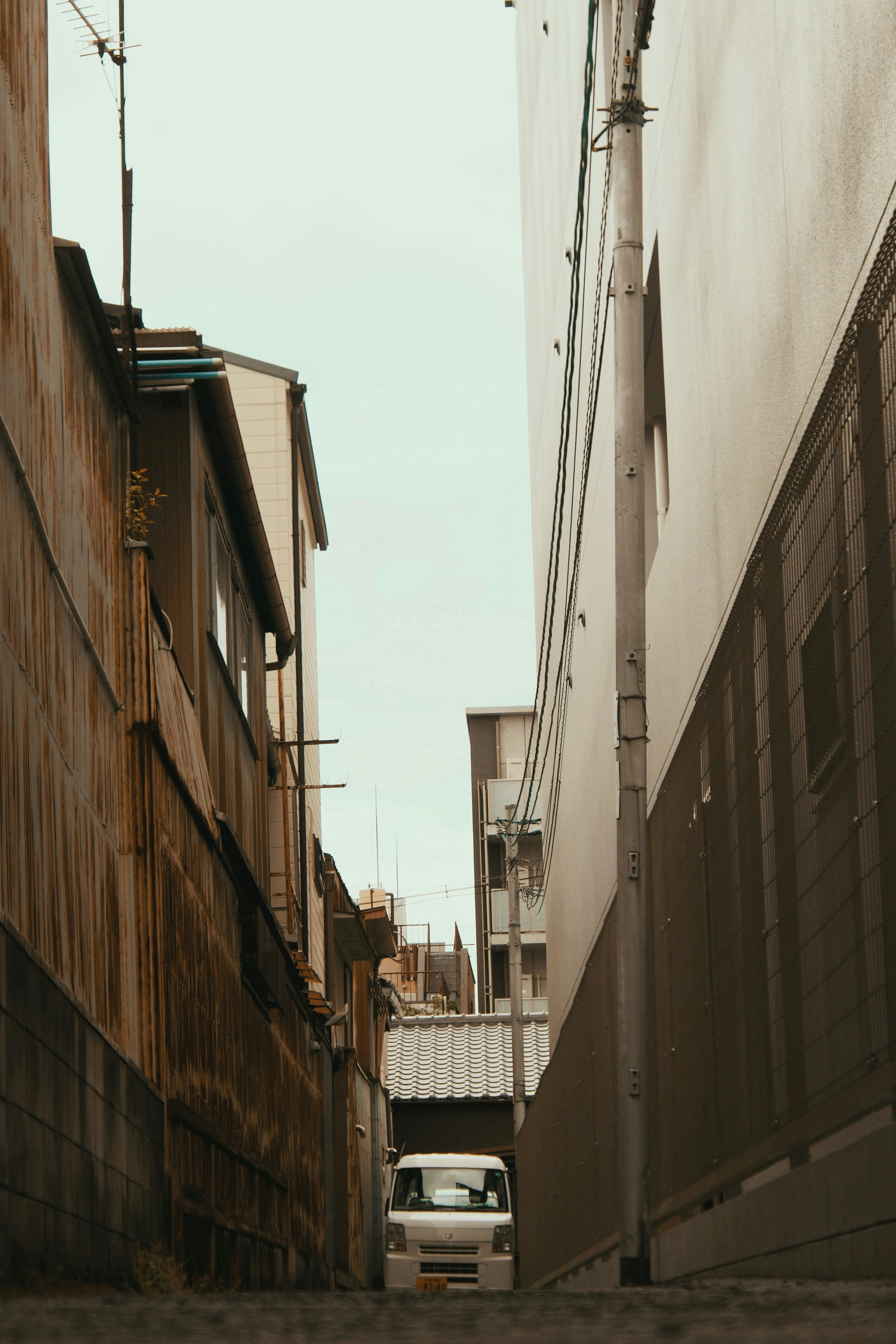 Narrow alleyway flanked by textured walls, leading to a partially obscured vehicle at the end. The scene captures the essence of urban exploration.