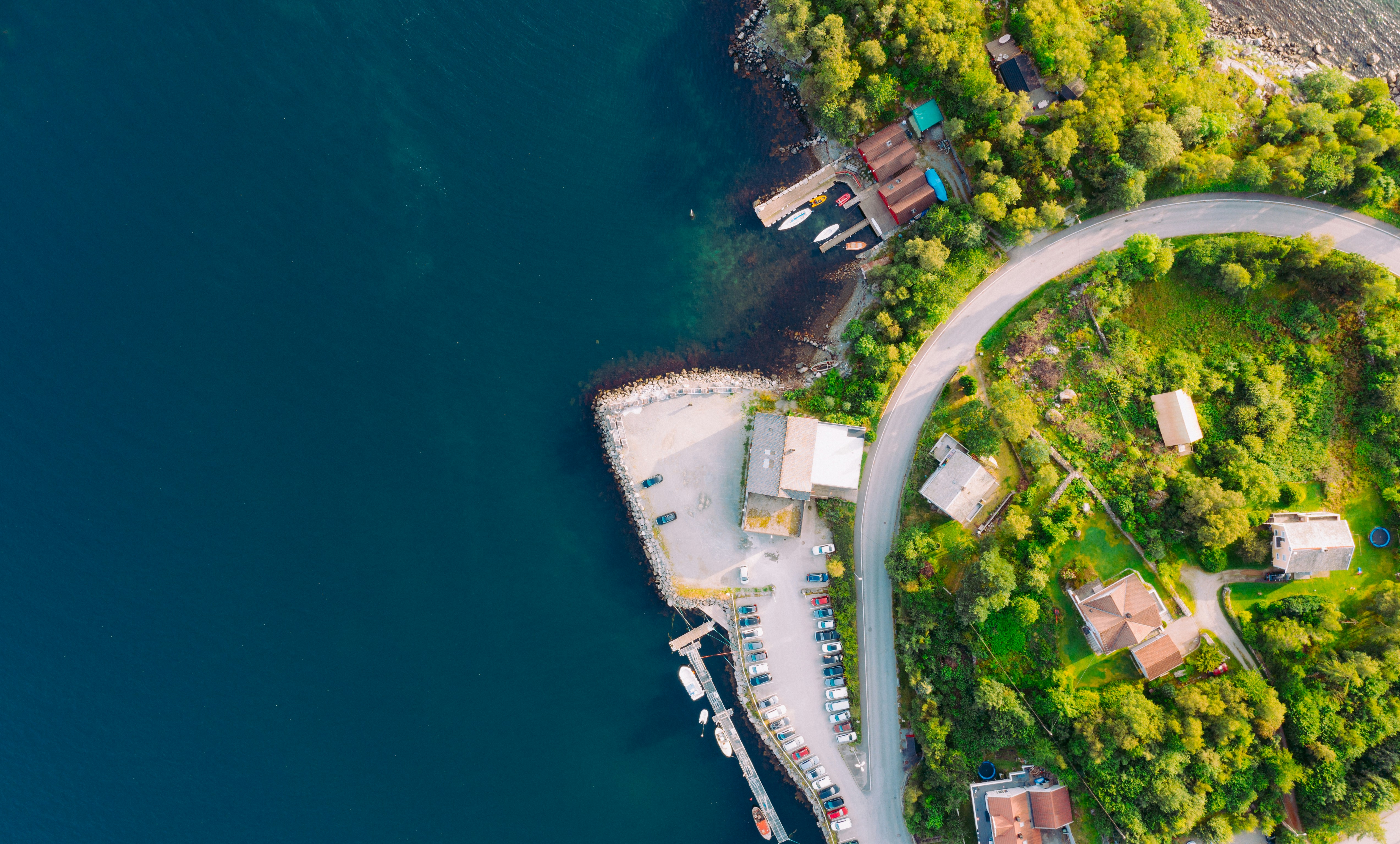 Aerial view of lush greenery and winding road meeting a serene coastline.