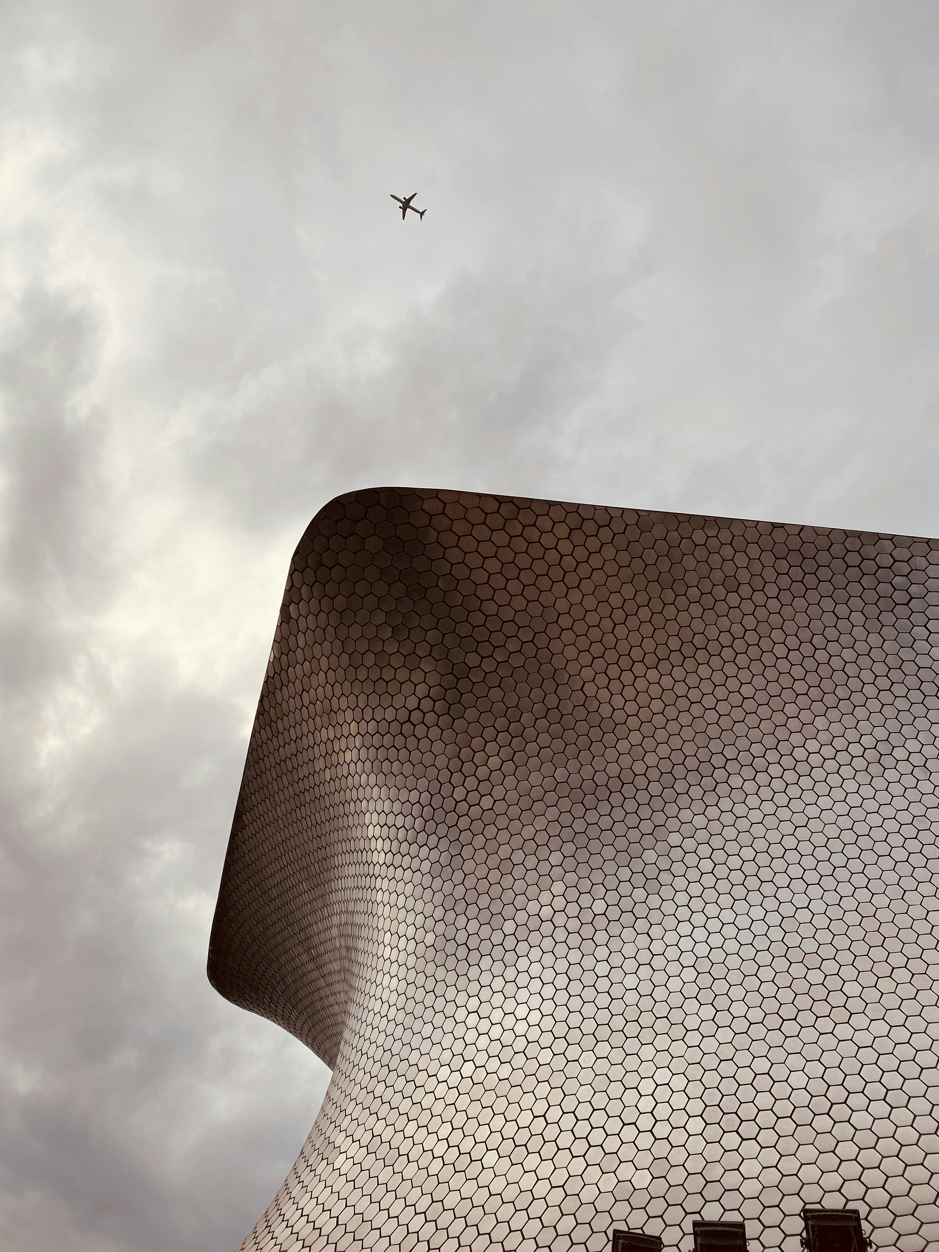 Copper Hex Skin Curling Upward as a Plane Drifts Across the Sky