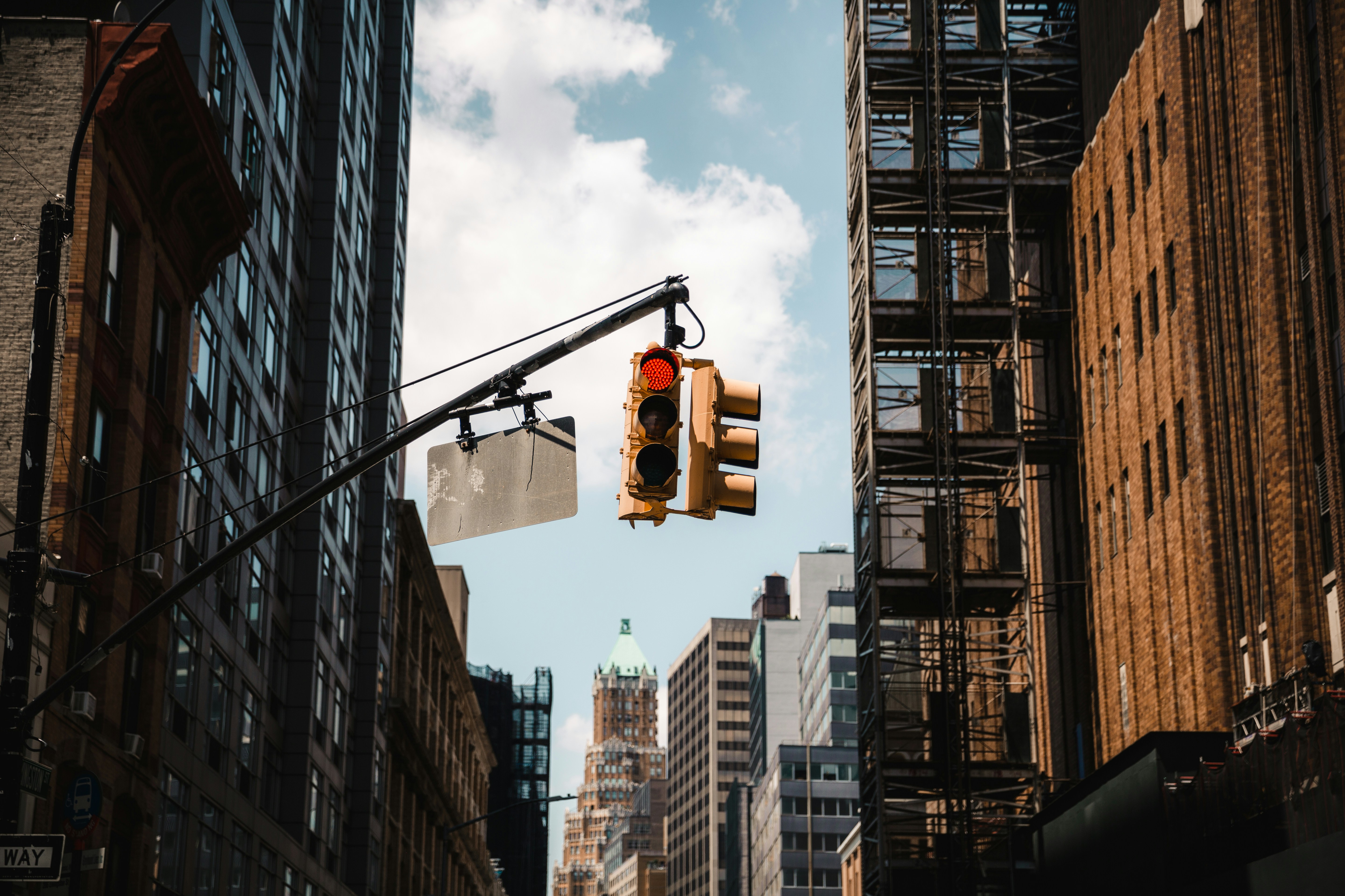 Traffic light hanging above a bustling urban street, framed by towering buildings and a dramatic sky.