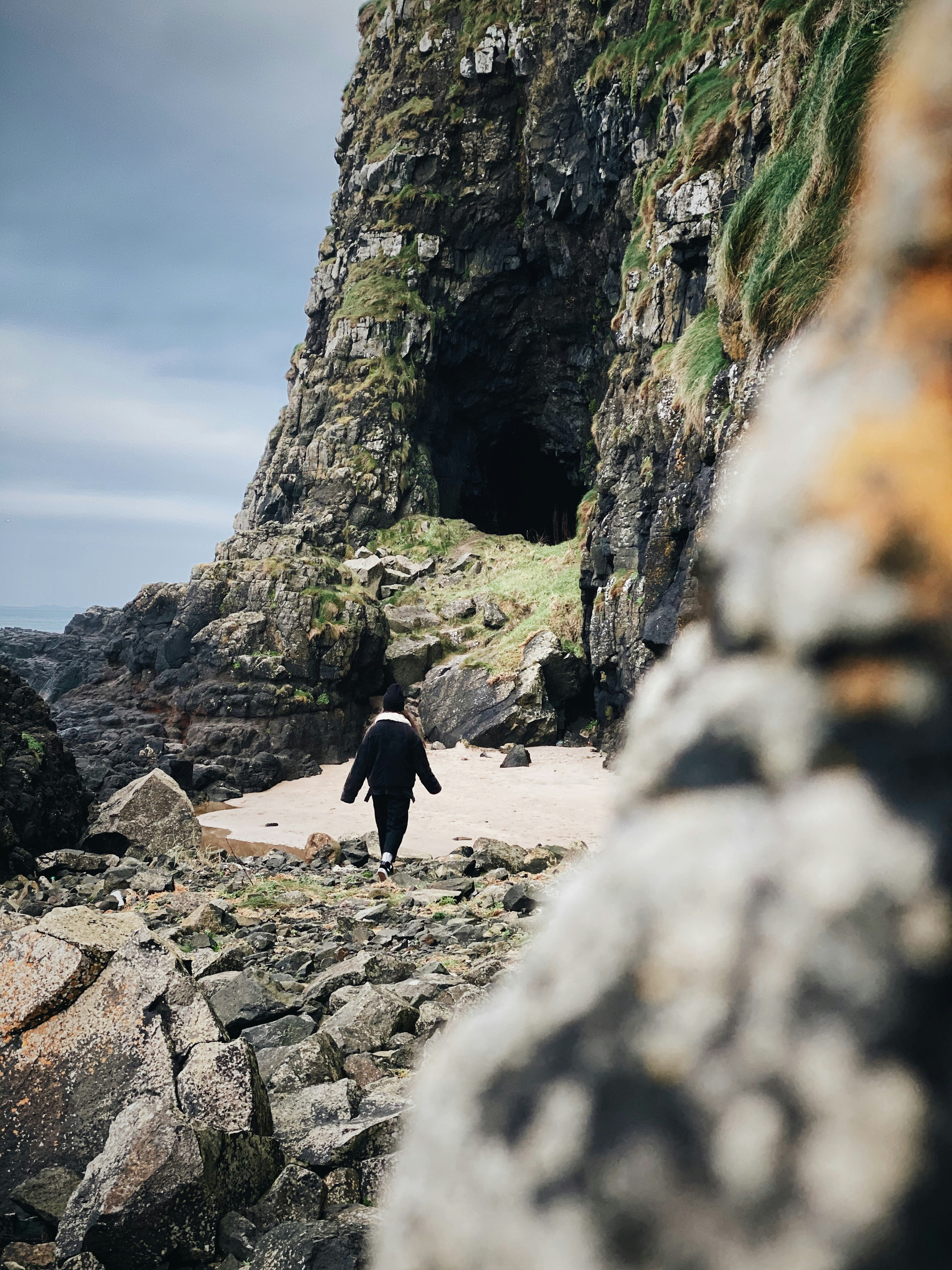 A solitary figure walks towards a secluded cove framed by towering cliffs and rugged rocks. The scene captures the essence of exploration and nature's majesty.