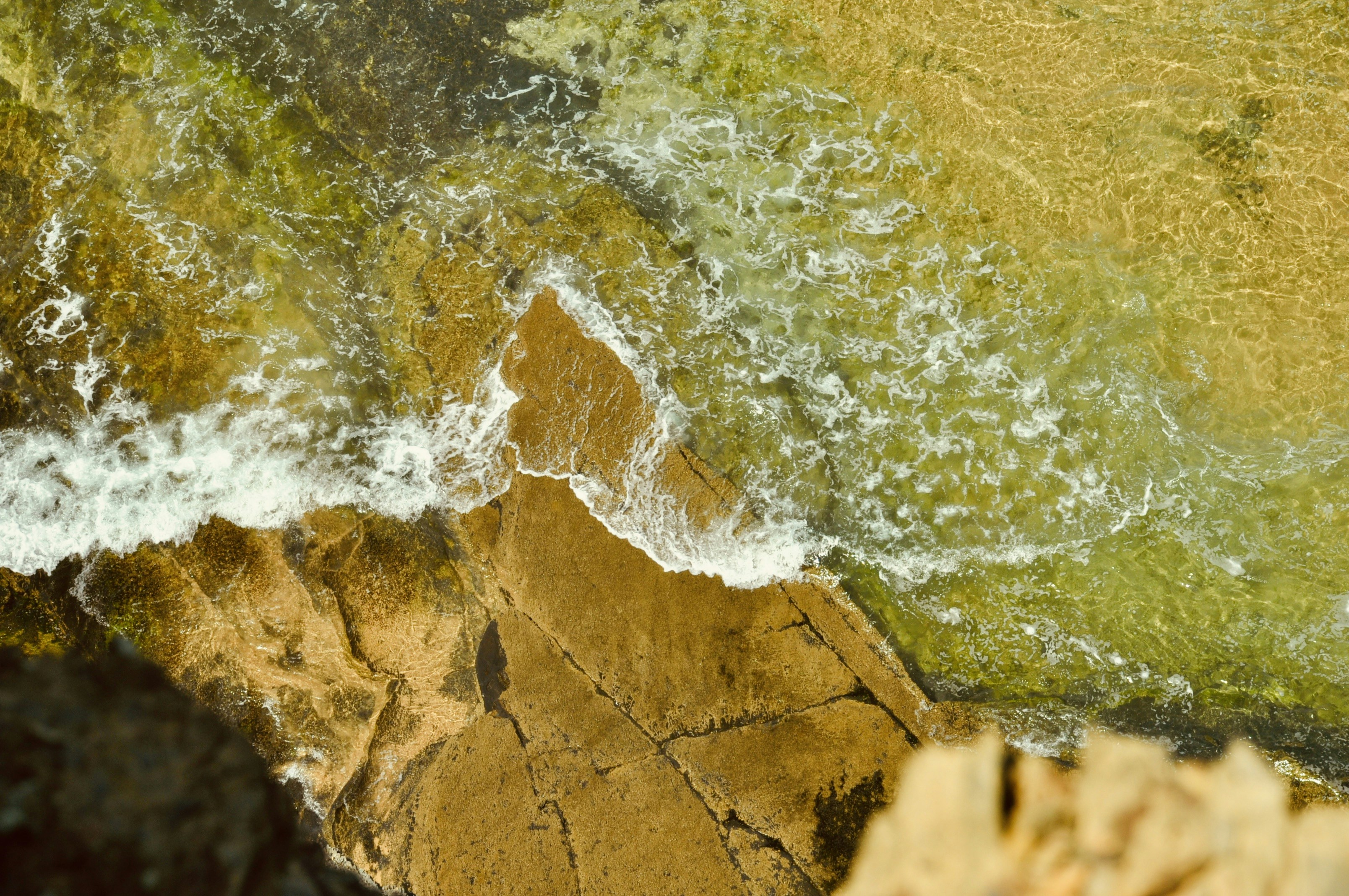 Waves gently washing over jagged coastal rocks beneath golden sunlight.