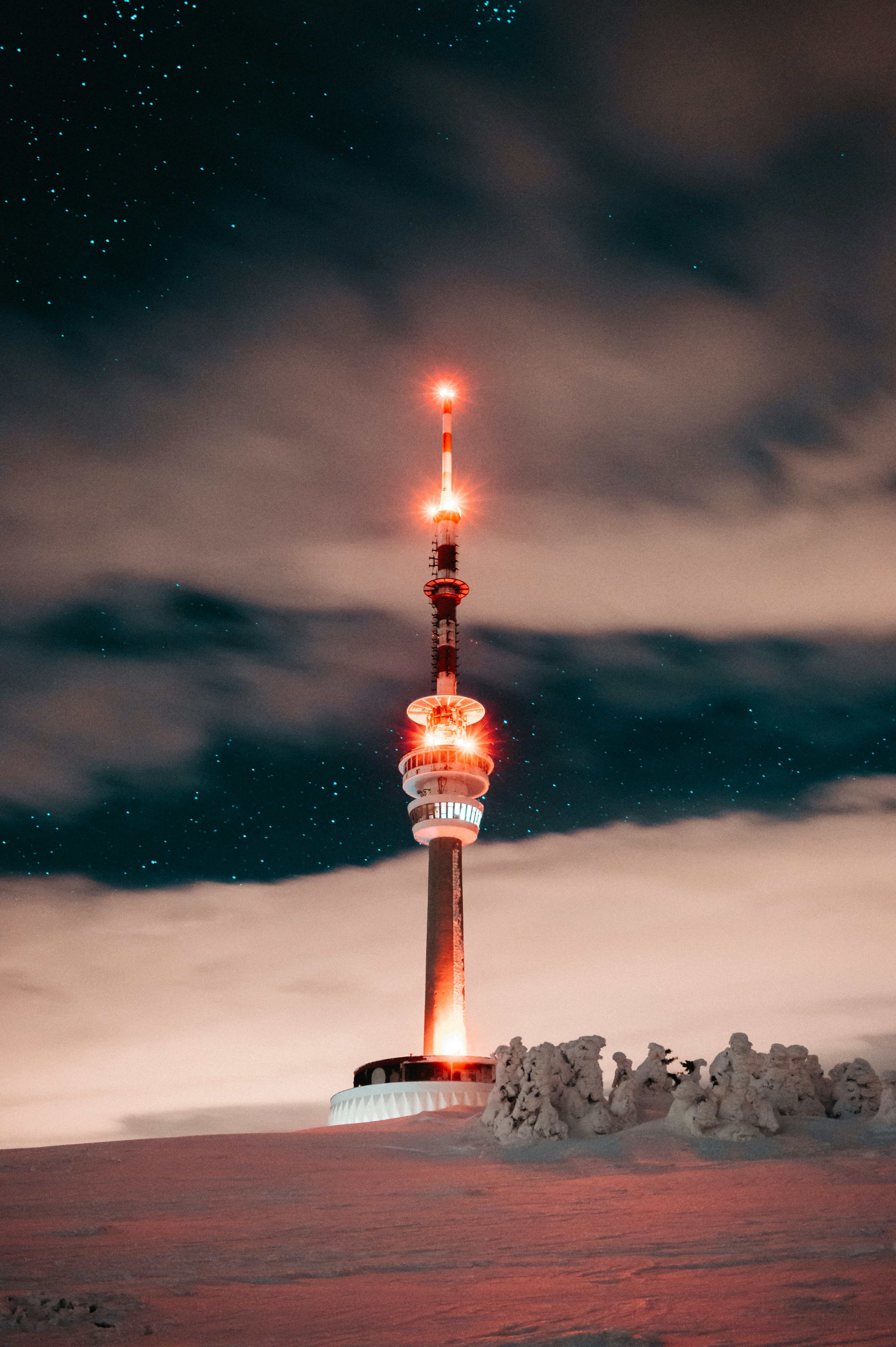 A communication tower stands tall against a starry sky, its lights glowing brightly amidst a snowy landscape.