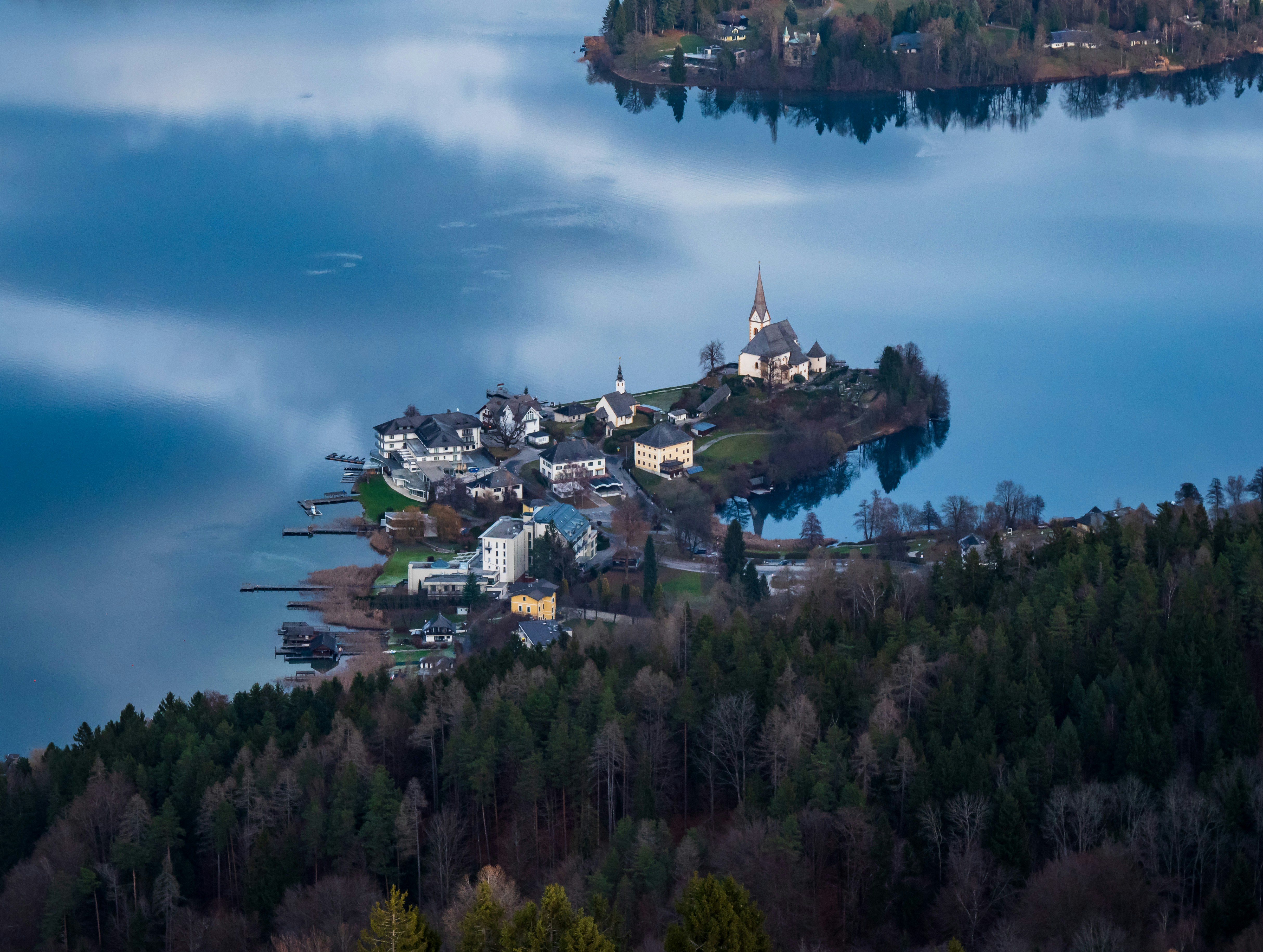 A tranquil island with a quaint village and church surrounded by calm blue waters and dense forests.