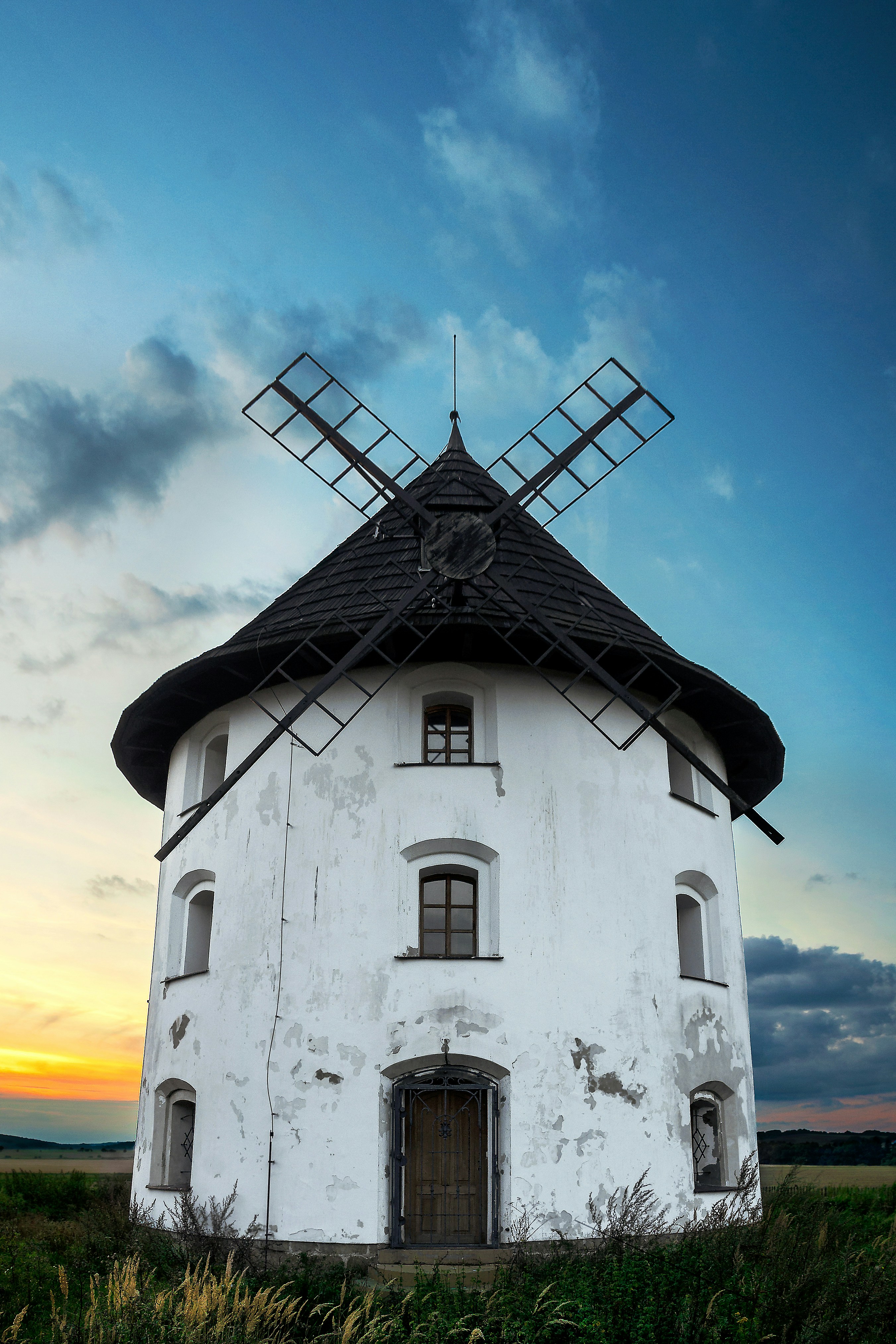 Crisscrossed Blades Above a Weathered White Windmill at Dusk