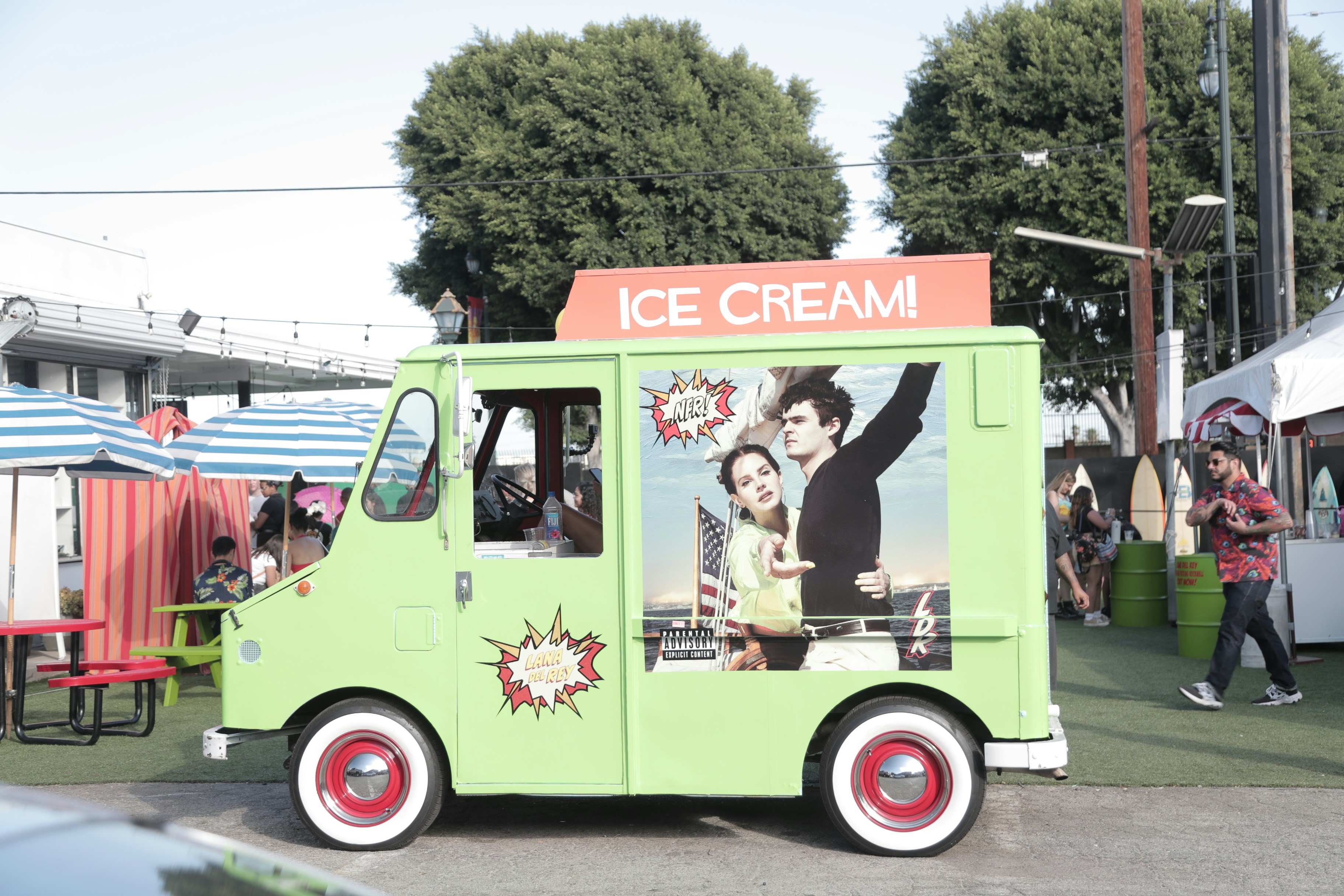 Green ice cream van with vintage artwork parked by colorful outdoor seating area.