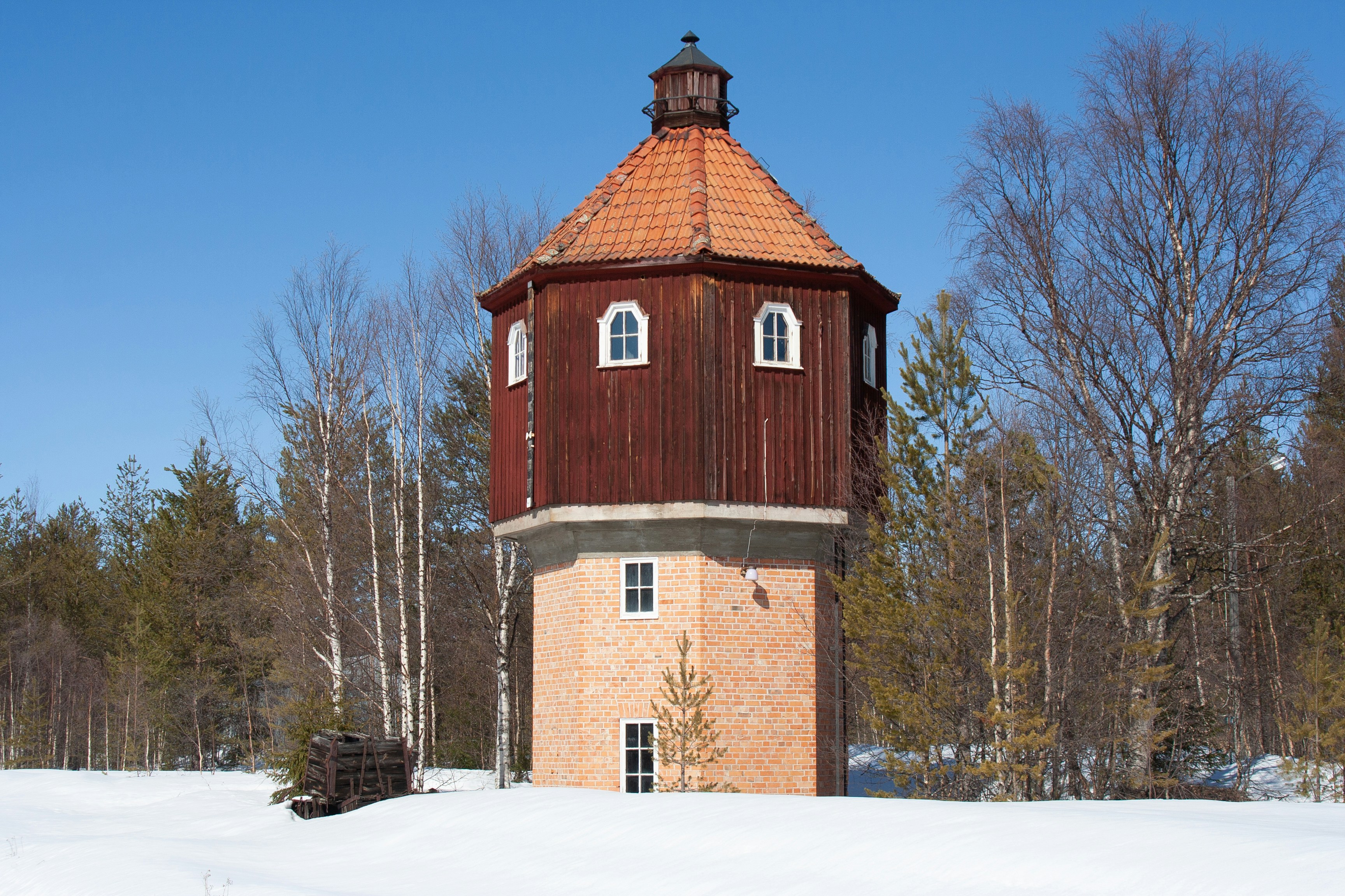 A vintage water tower stands tall in a snowy landscape, surrounded by sparse trees under a clear blue sky.