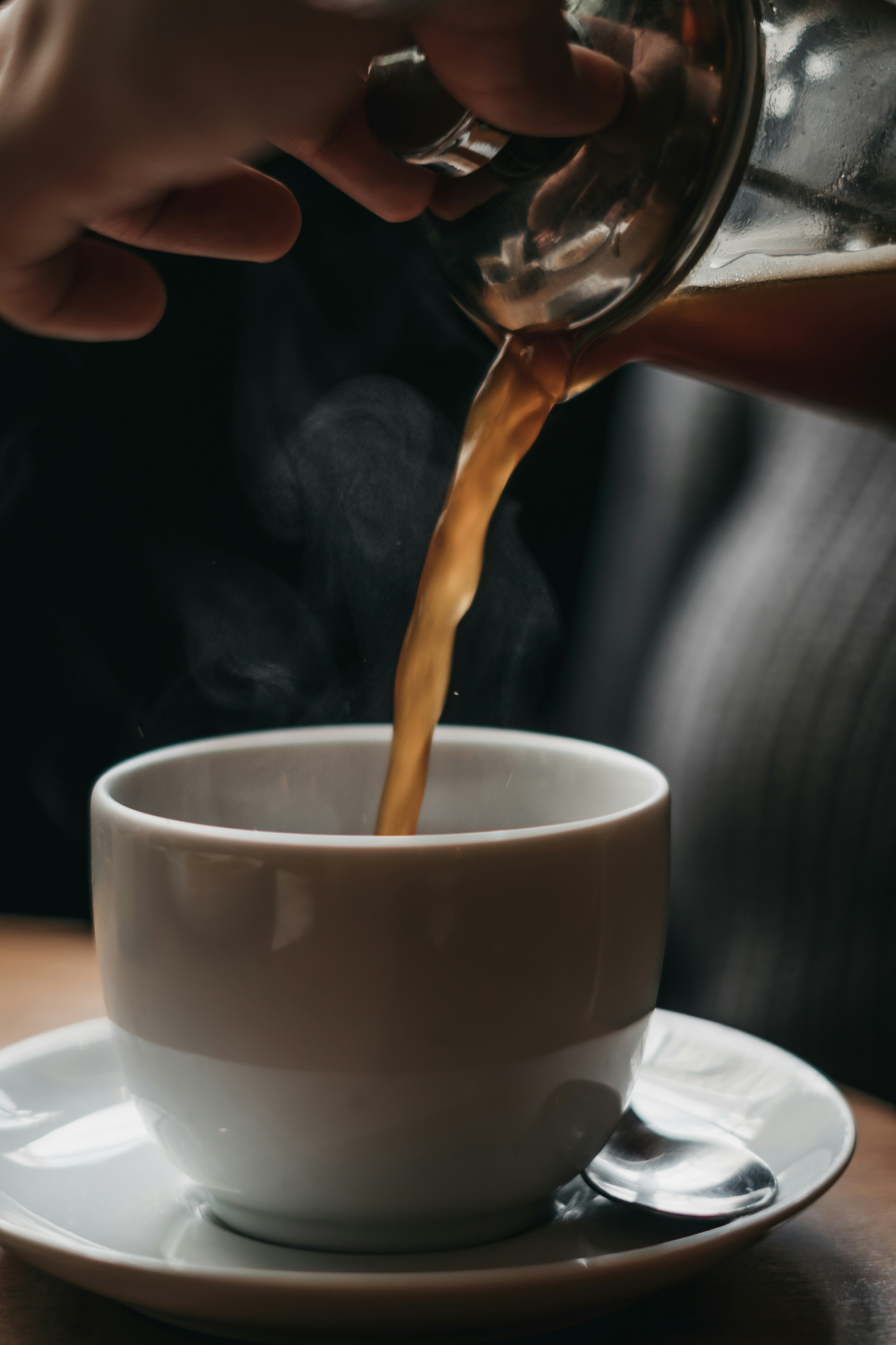 Coffee being poured into a white cup, steam rising in the air, creating a cozy atmosphere. The scene captures the essence of a tranquil coffee ritual.