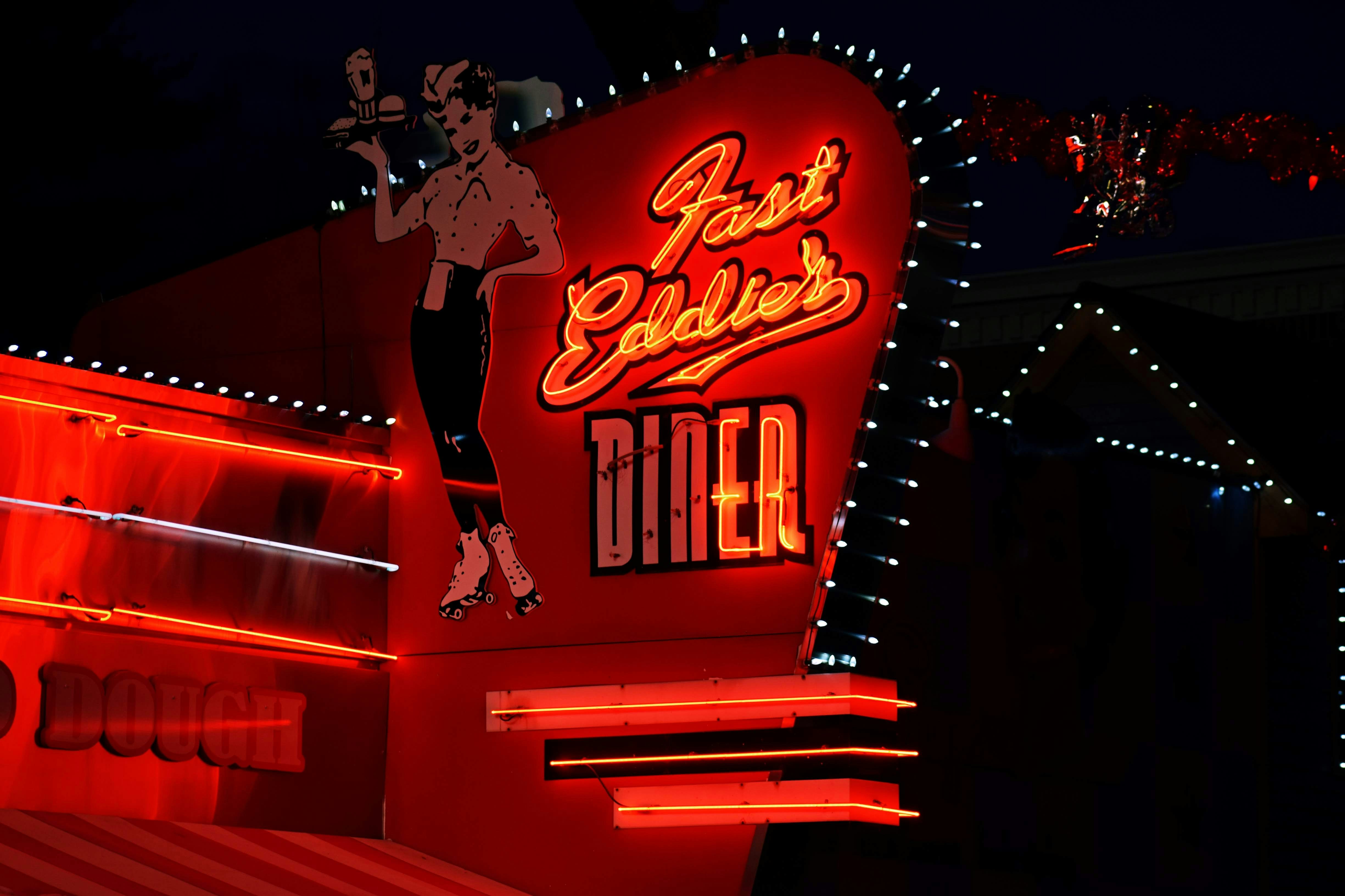 Bright neon sign of Fast Eddie's Diner illuminated against the night sky, featuring retro-styled lettering and classic diner imagery.